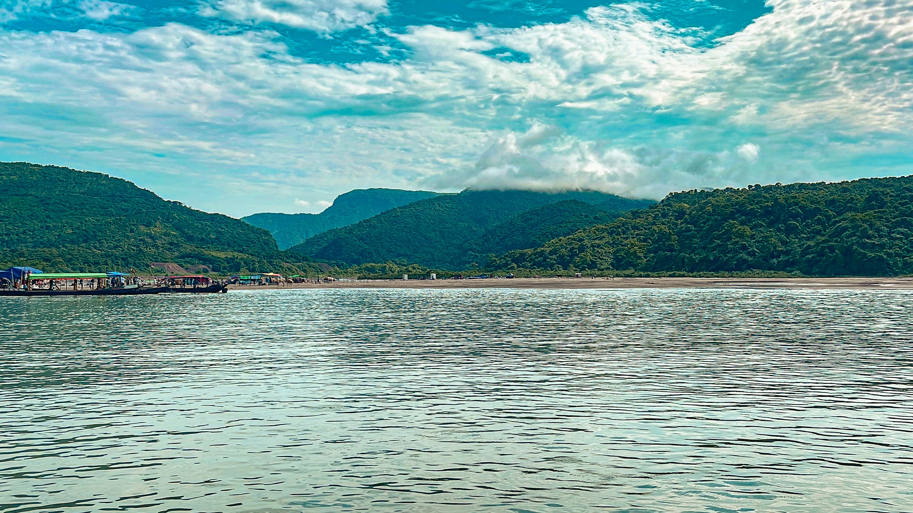 Expansive river with lush green hills under a partly cloudy sky.