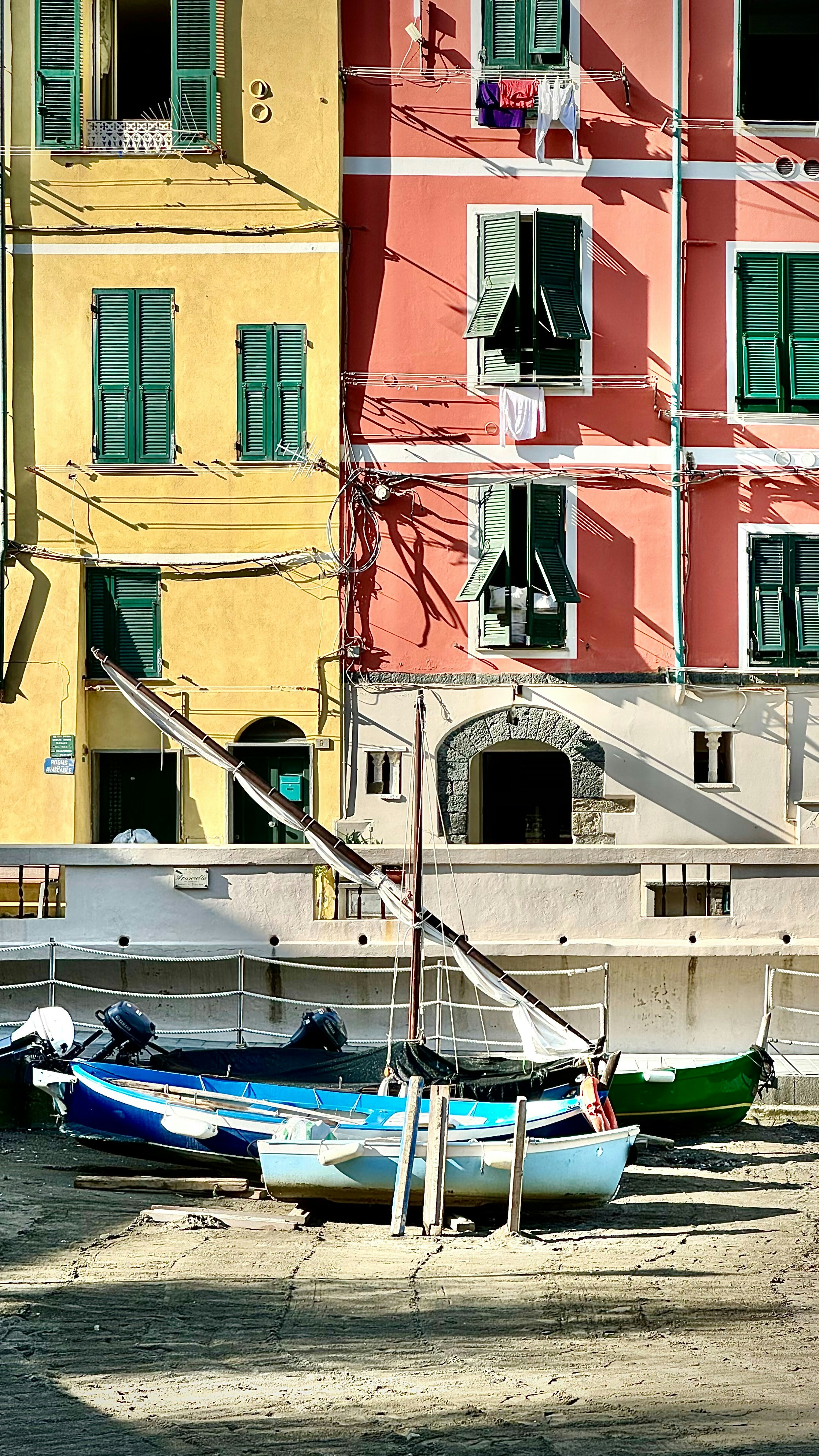 Colorful yellow and red building façades flank a small harbor, with green shutters and moored boats along the quay.