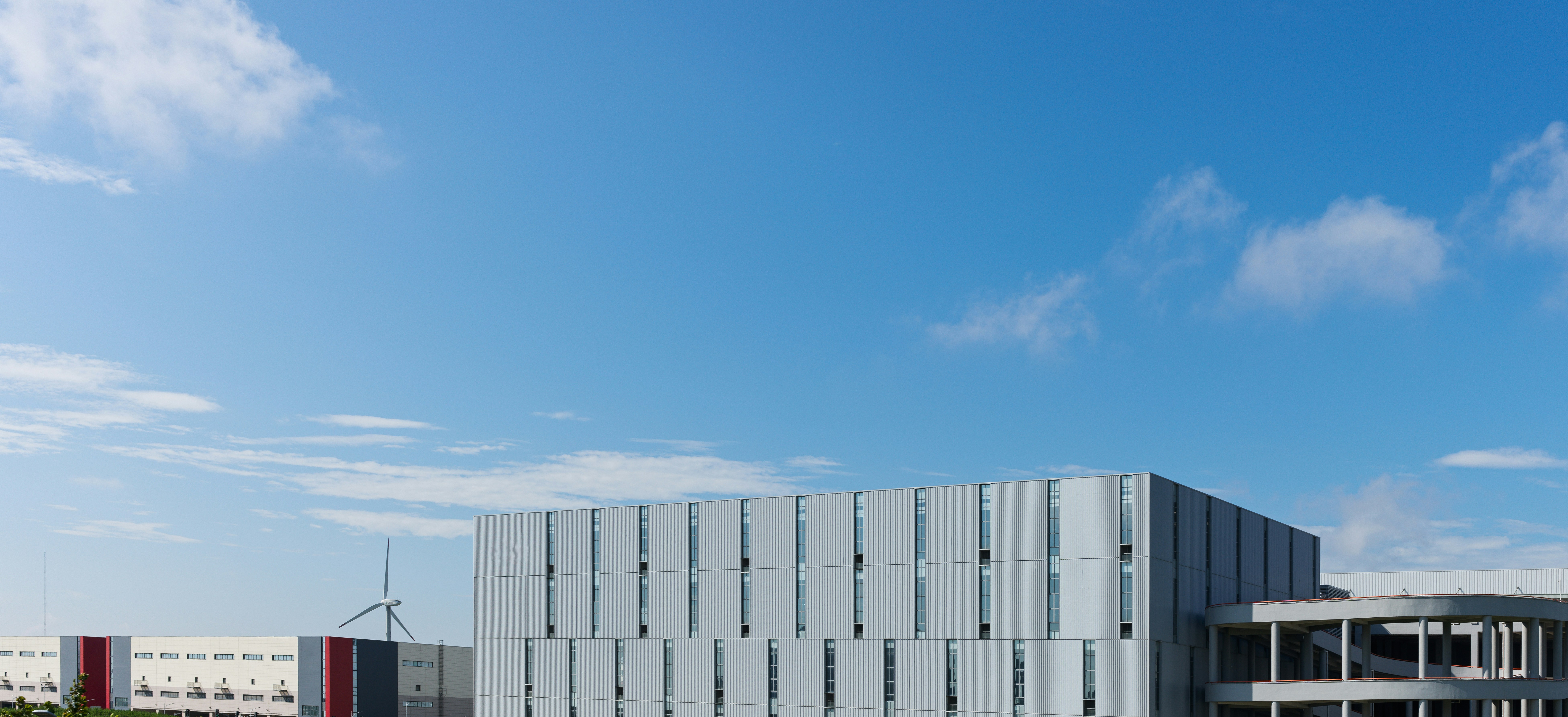 Wide view of modern industrial buildings with modular gray façades beneath a bright blue sky, emphasizing geometric repetition.