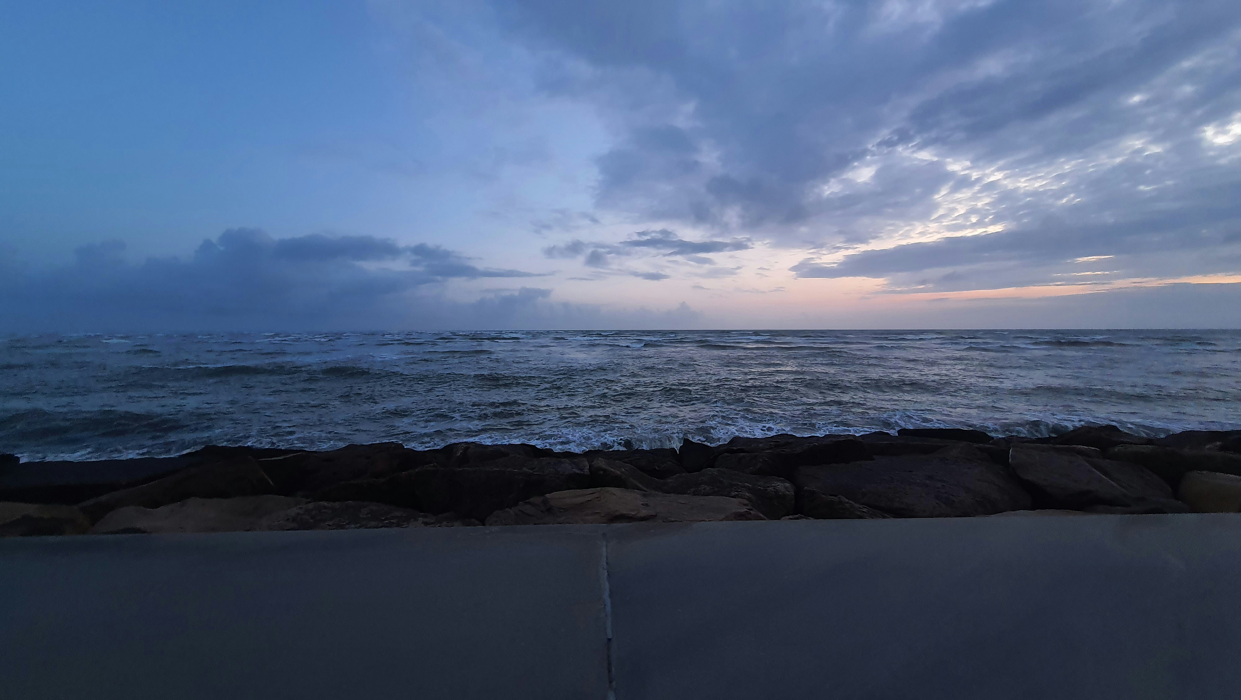 Waves crashing against a rocky shoreline under a cloudy evening sky.