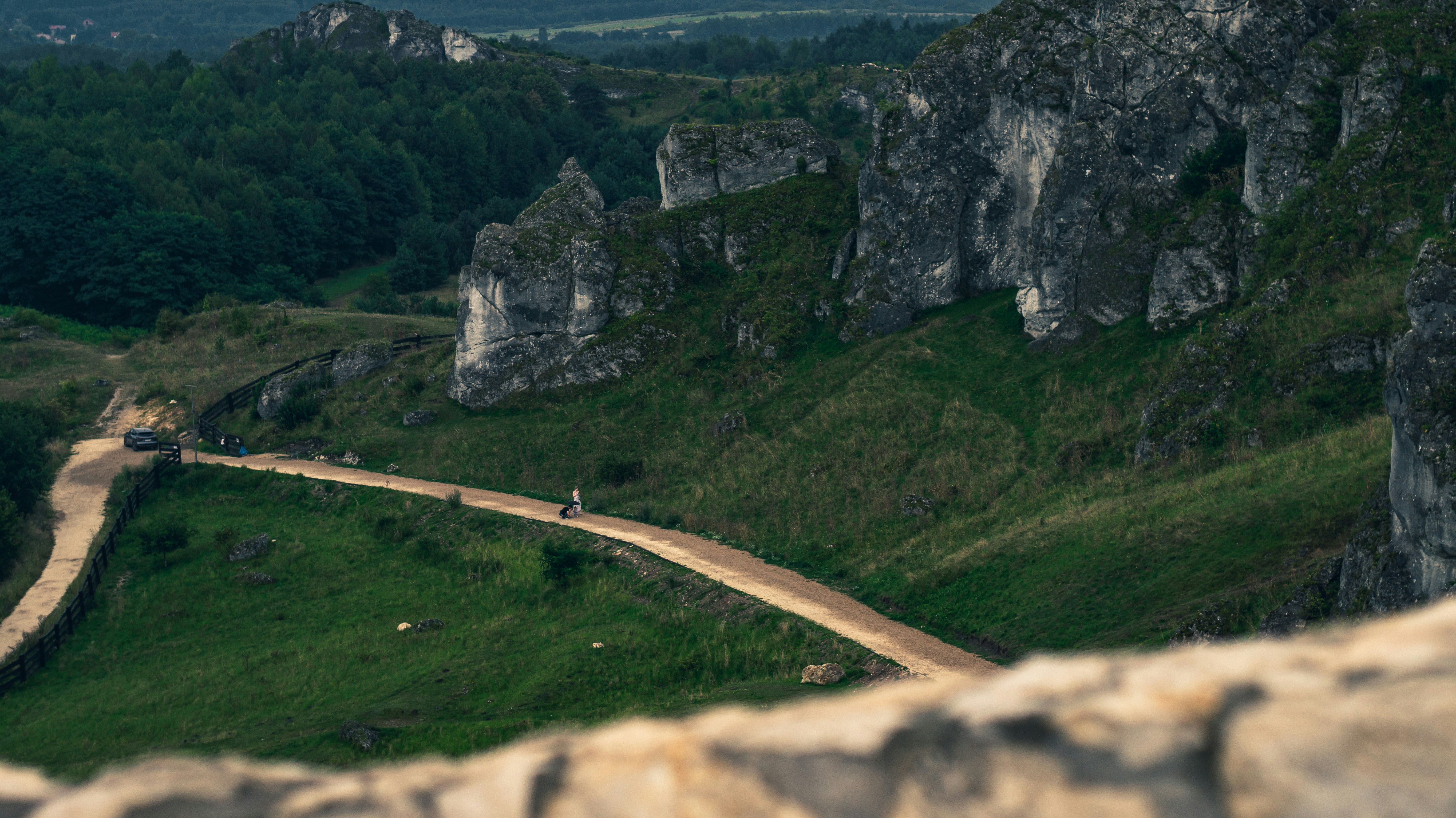 Curved dirt road leading through lush green landscape flanked by rugged limestone cliffs.