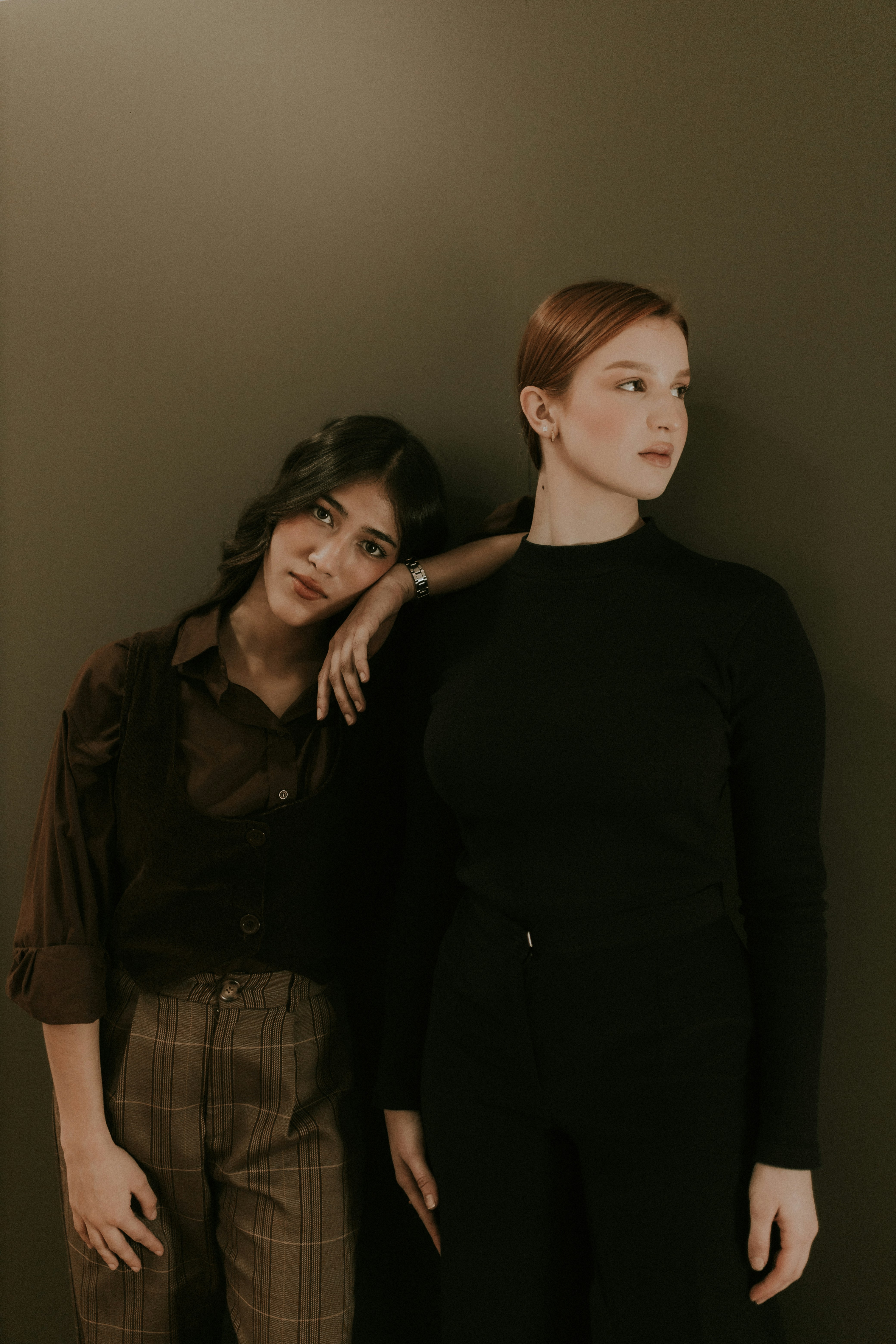 Two women standing next to each other near a wall
