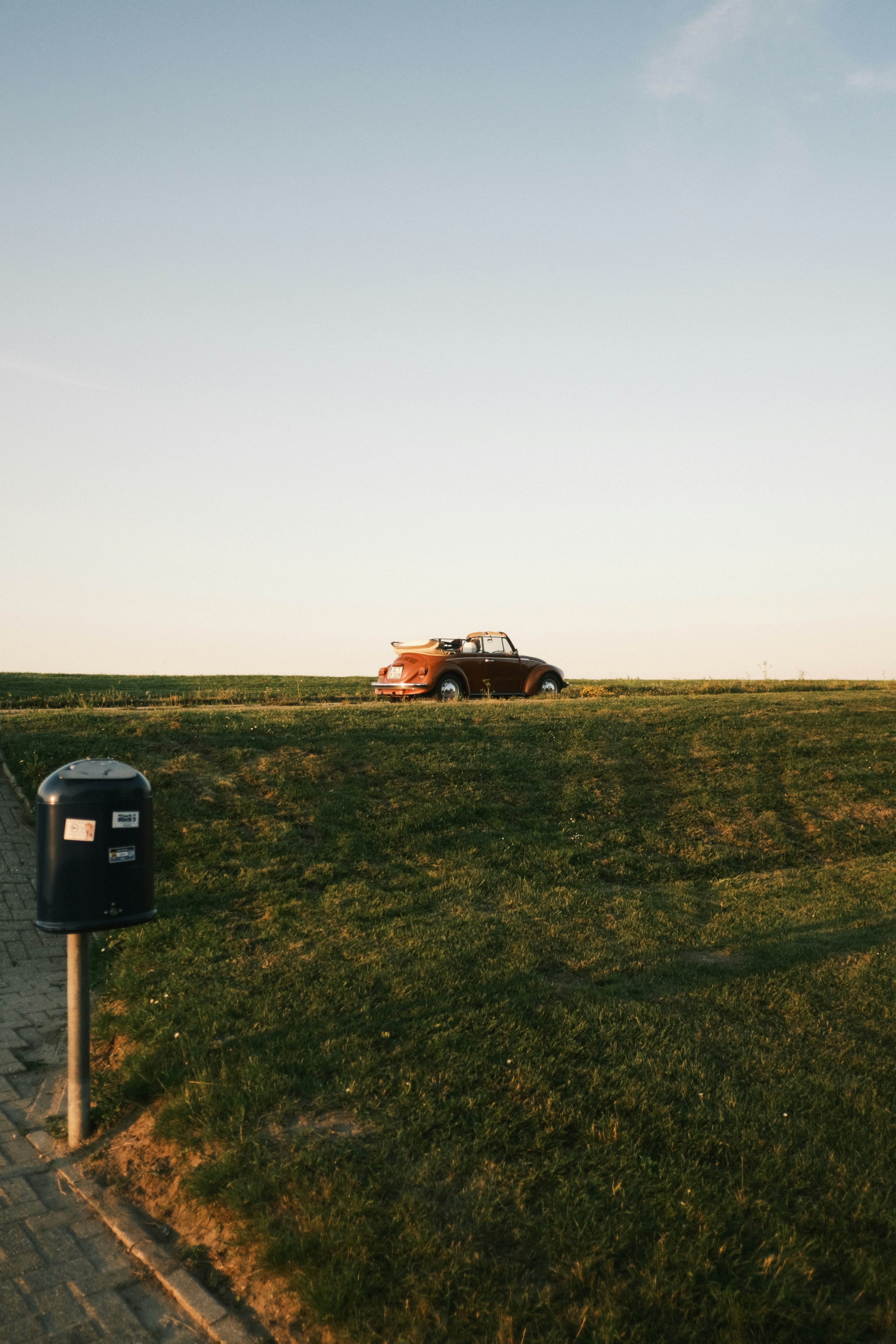 A photograph captures a red vintage convertible on a grassy hill, with a foreground mailbox and a wide, clear sky.