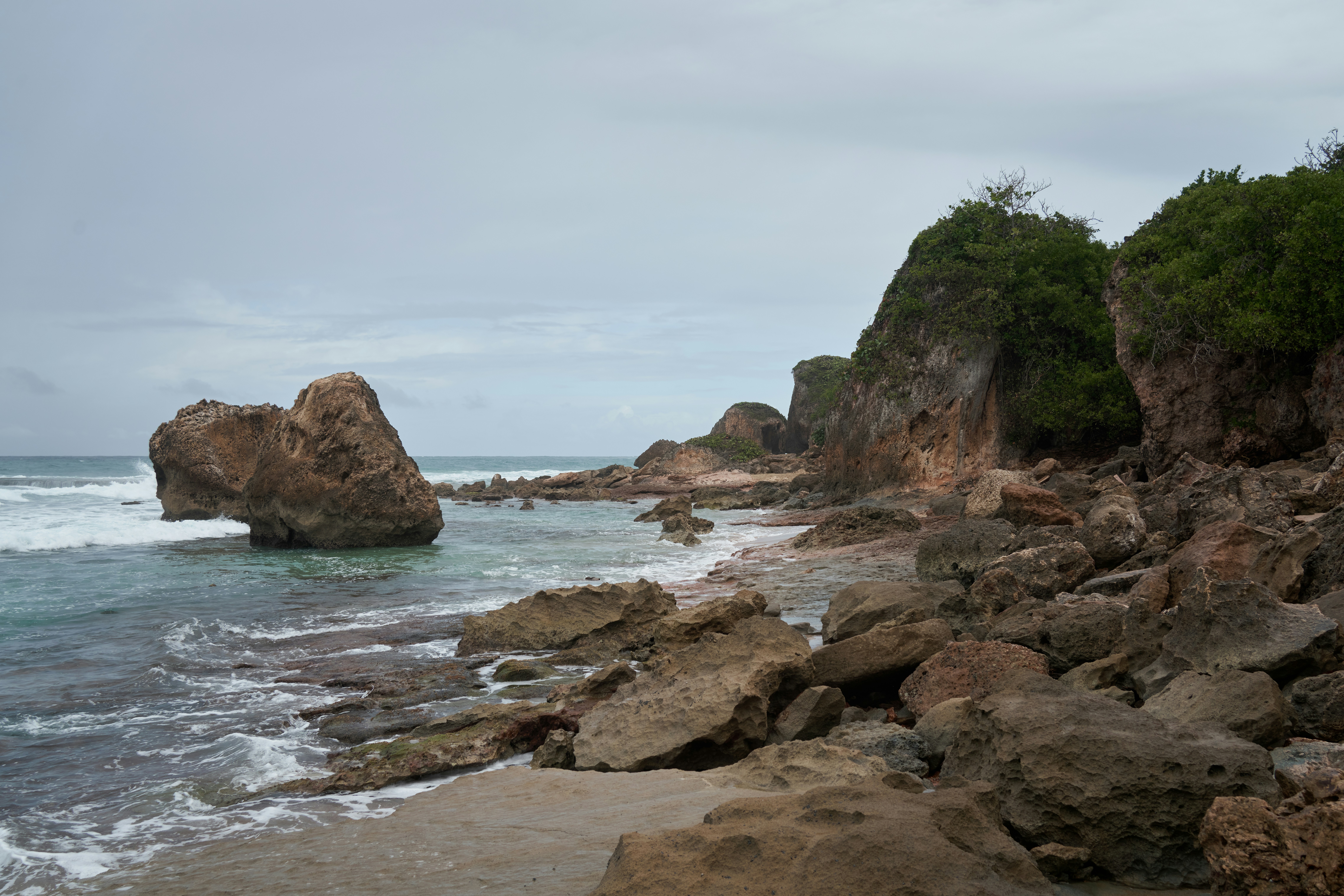 Rocky shoreline with large formations and waves under a cloudy sky.