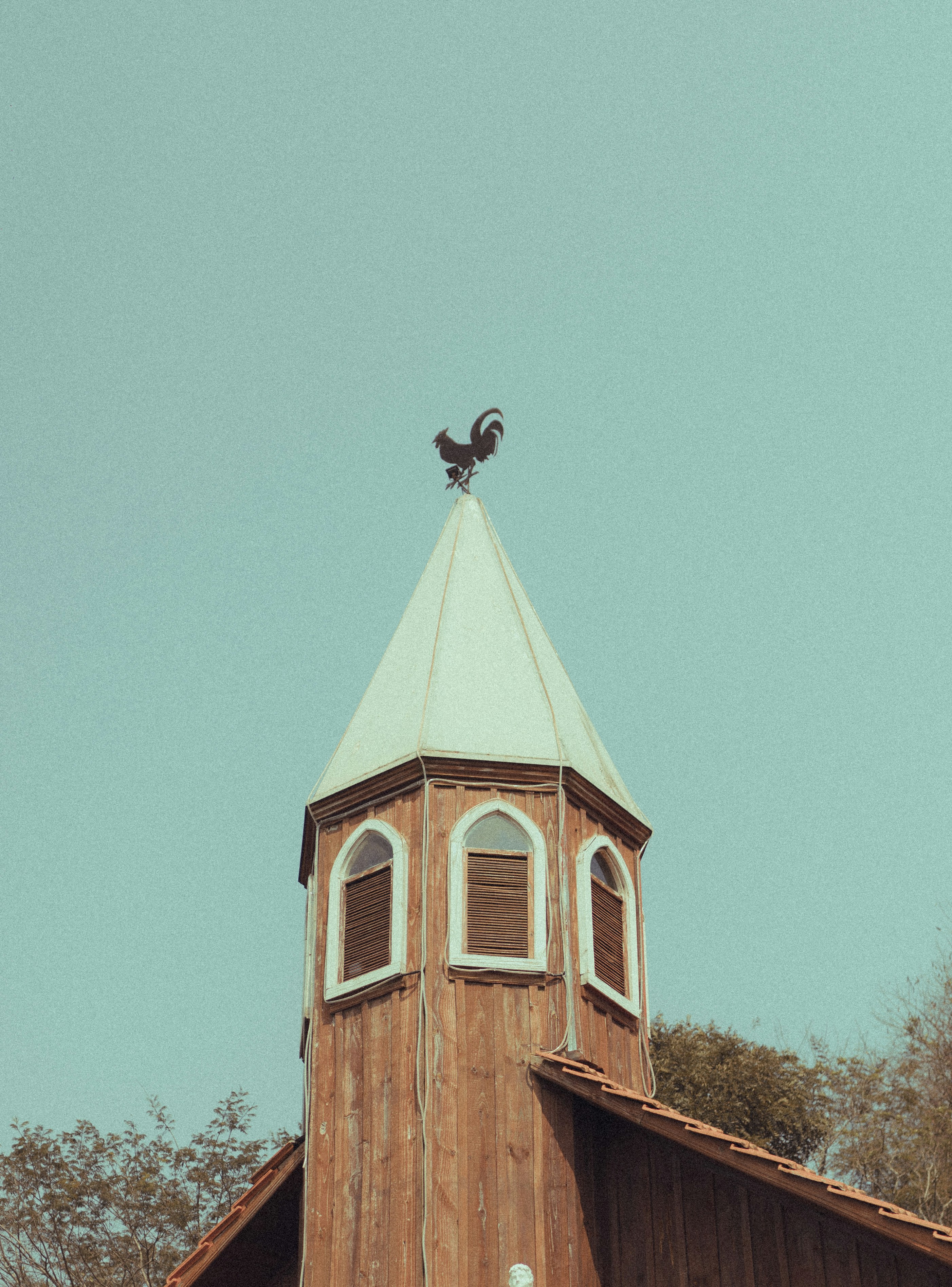 Rooster at the Peak: A Weathered Church Tower Under a Mint Sky