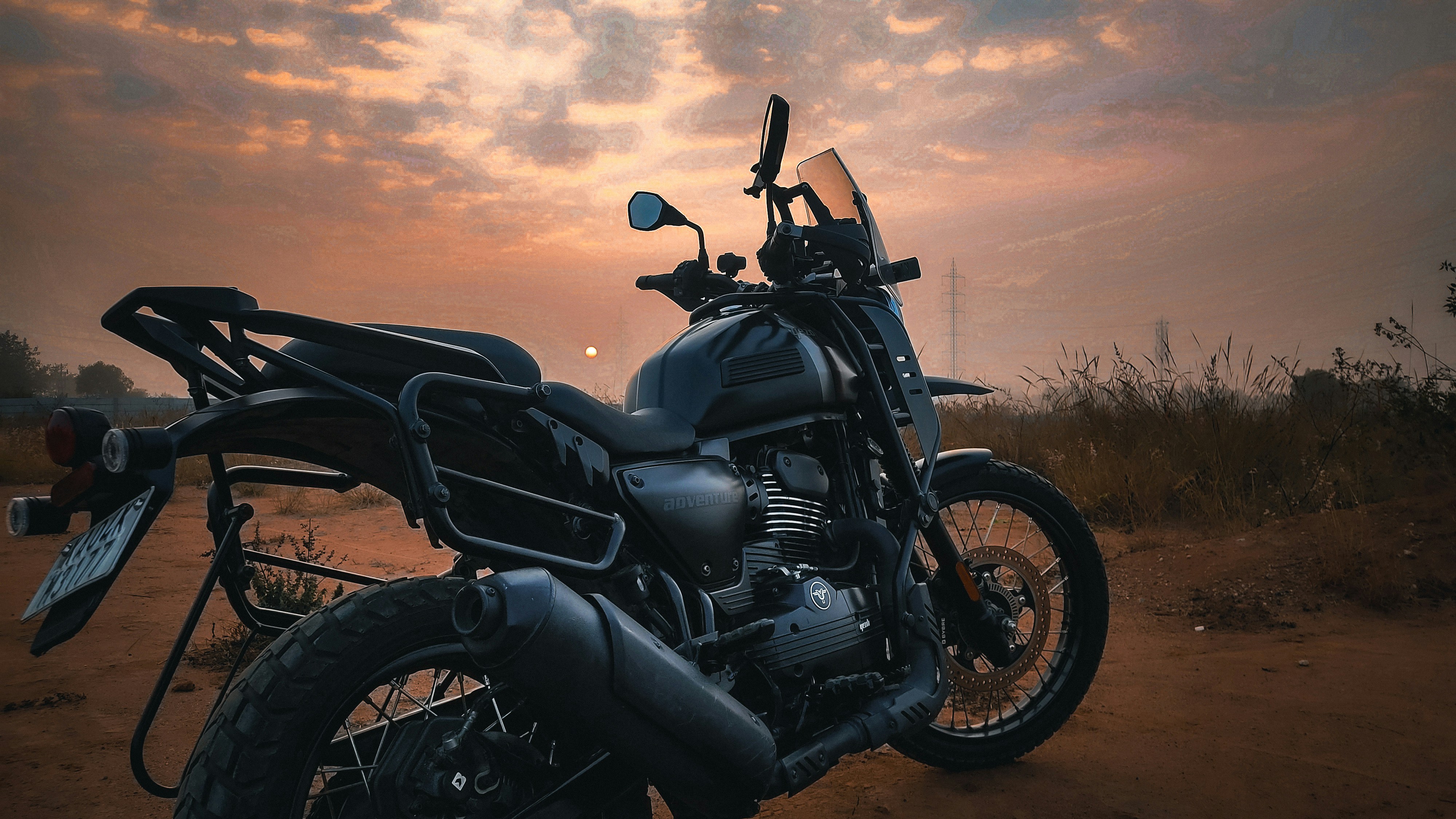 Photograph of a rugged adventure motorcycle parked on a dusty plain with a warm sunset glow.