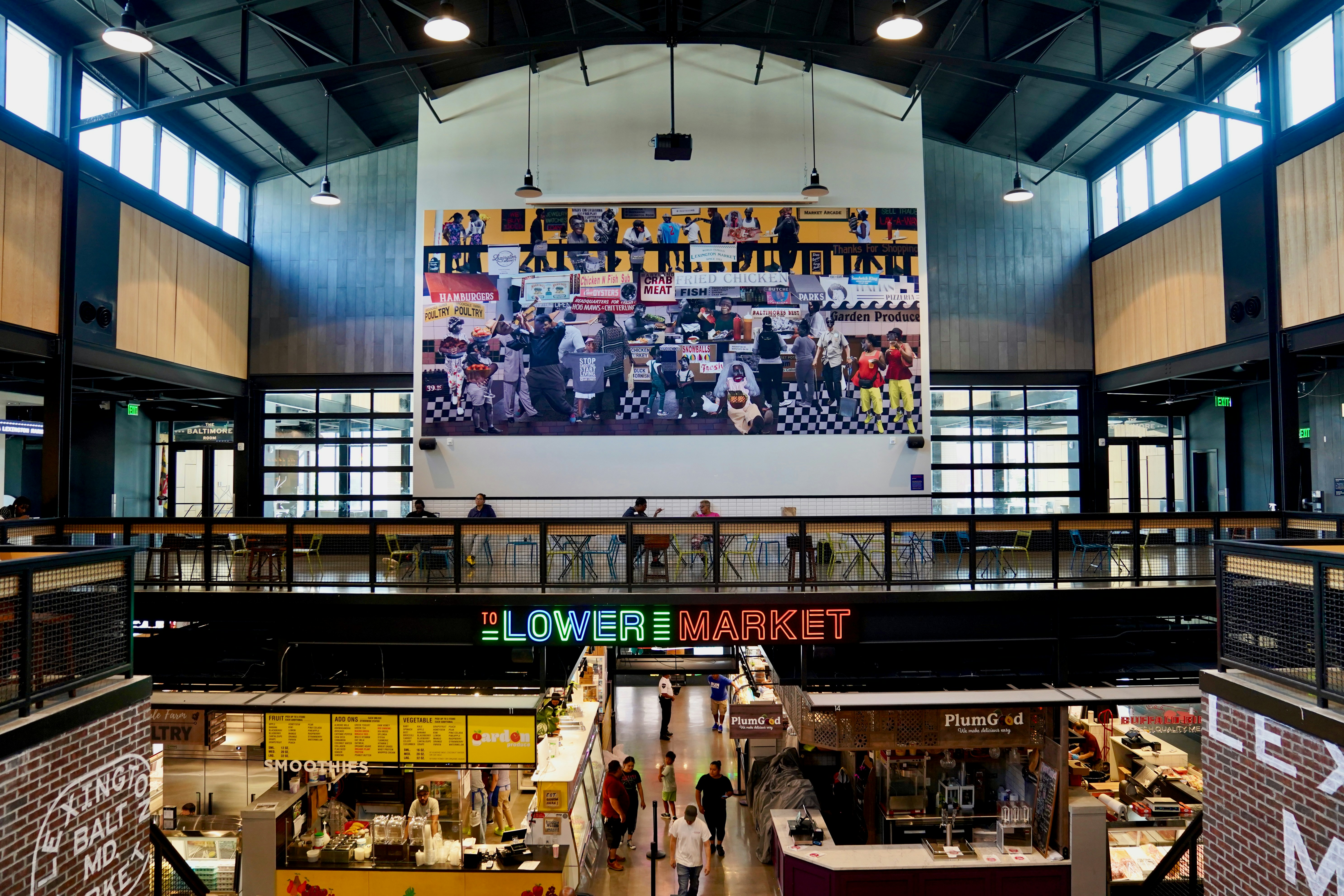 Interior of a bustling market hall with people moving among various stalls under a large central artwork.