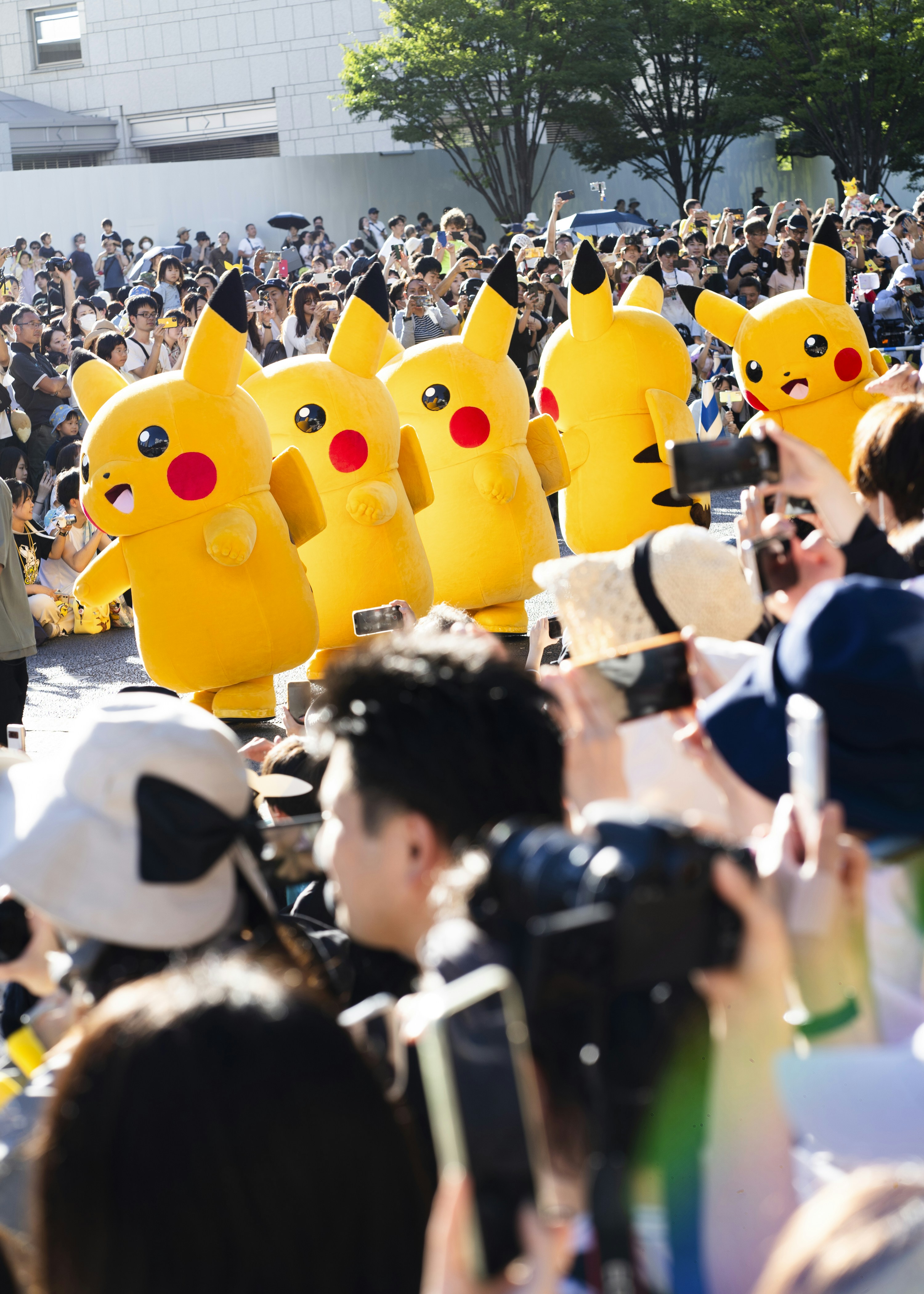 A large crowd of people with pokemon balloons in the shape of pikachu ...