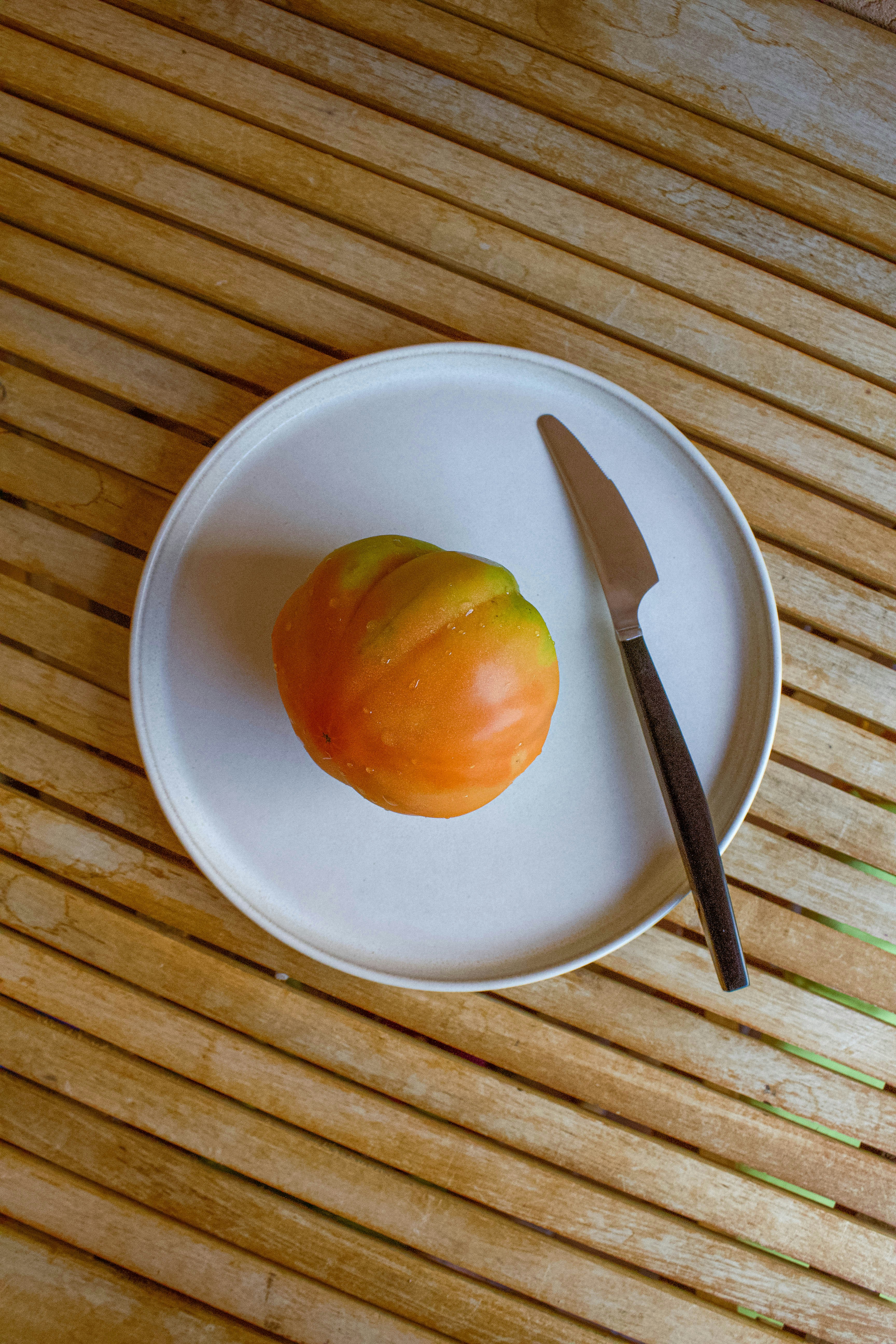 A white plate topped with an orange next to a knife and fork
