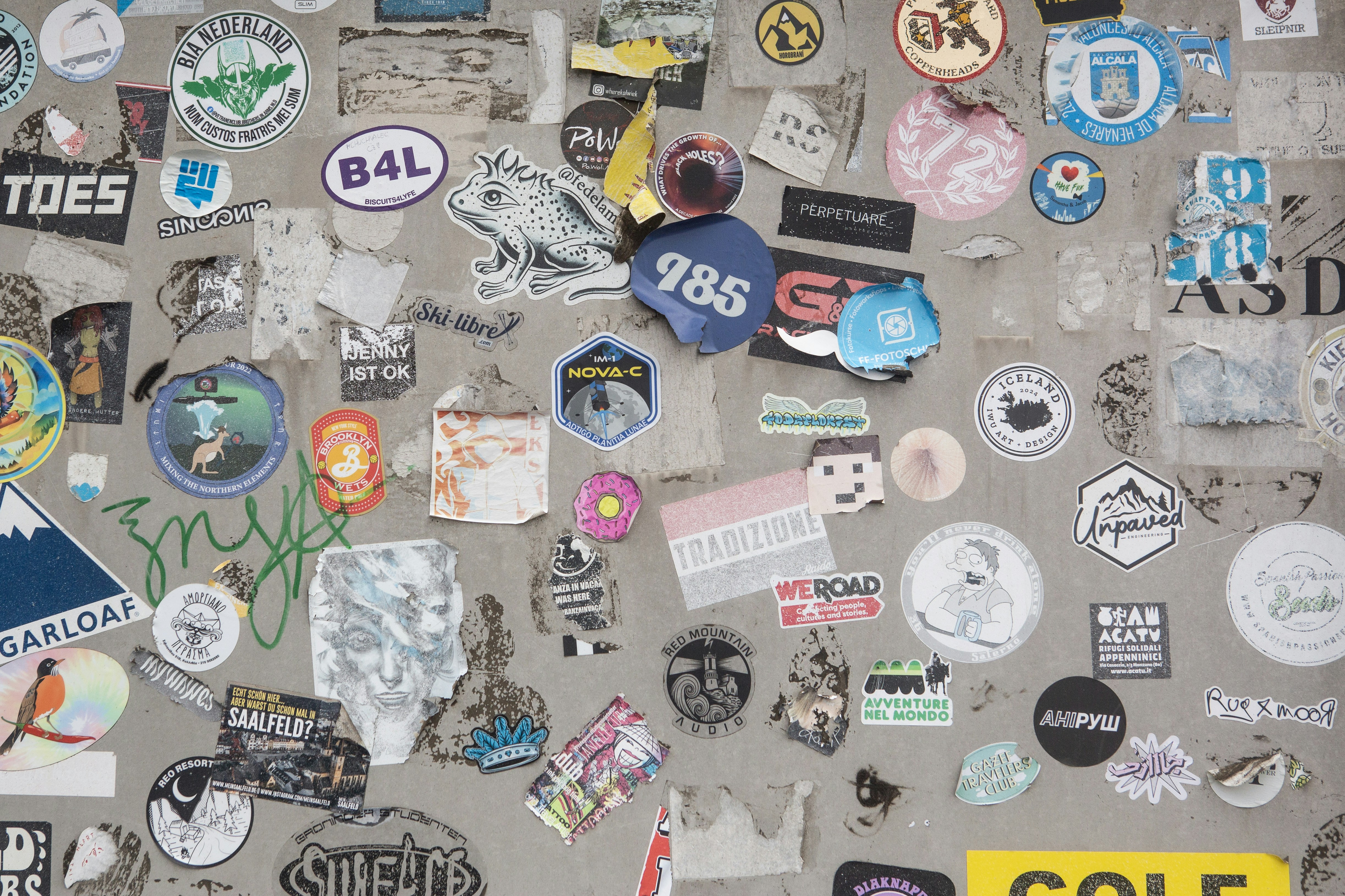 A vibrant collage of various stickers plastered on a weathered surface, showcasing a blend of colors and designs. The assortment reflects personal expressions and cultural references.