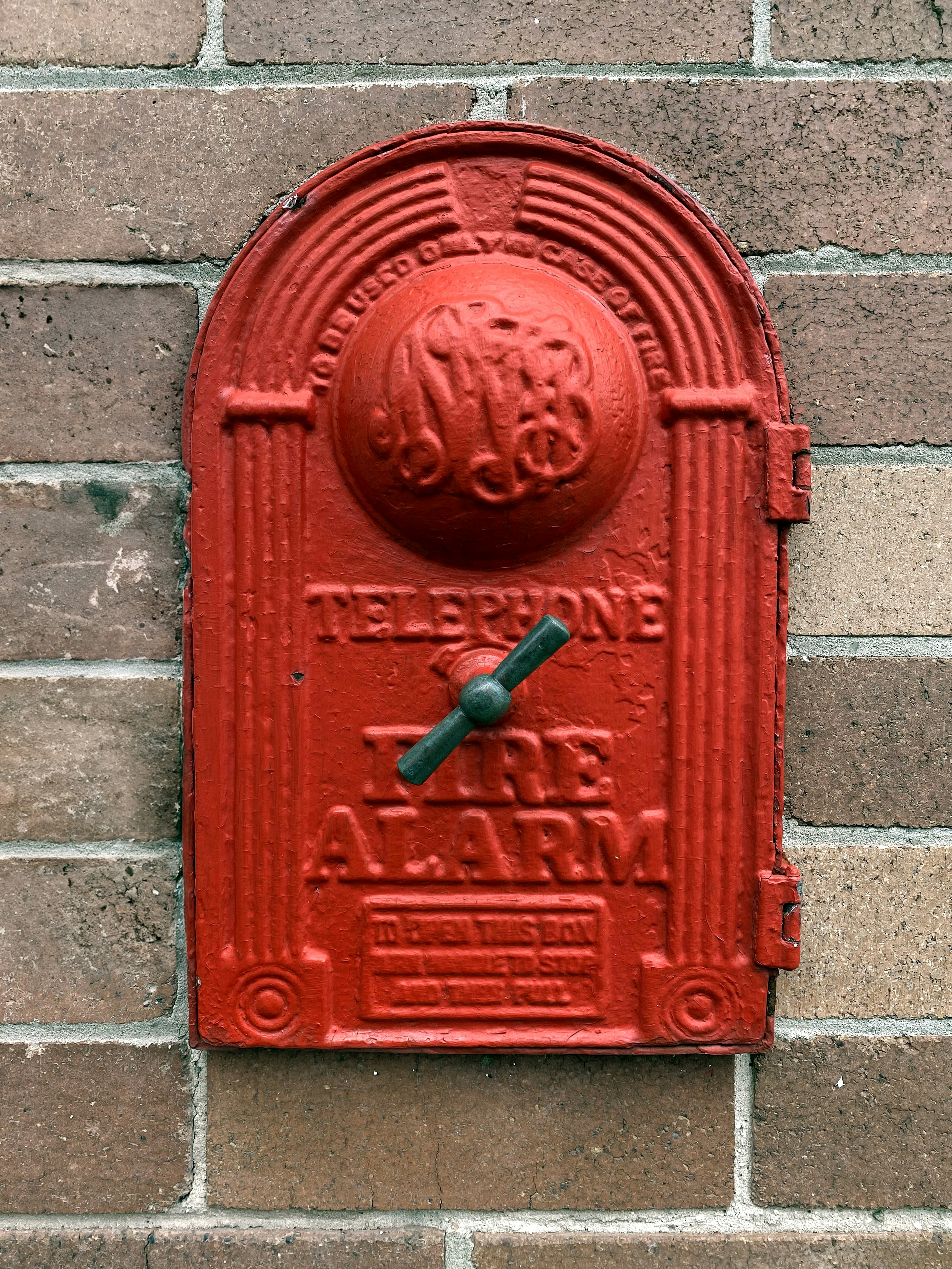 Bright red fire alarm box mounted on a brick wall, showcasing vintage design and historical significance.