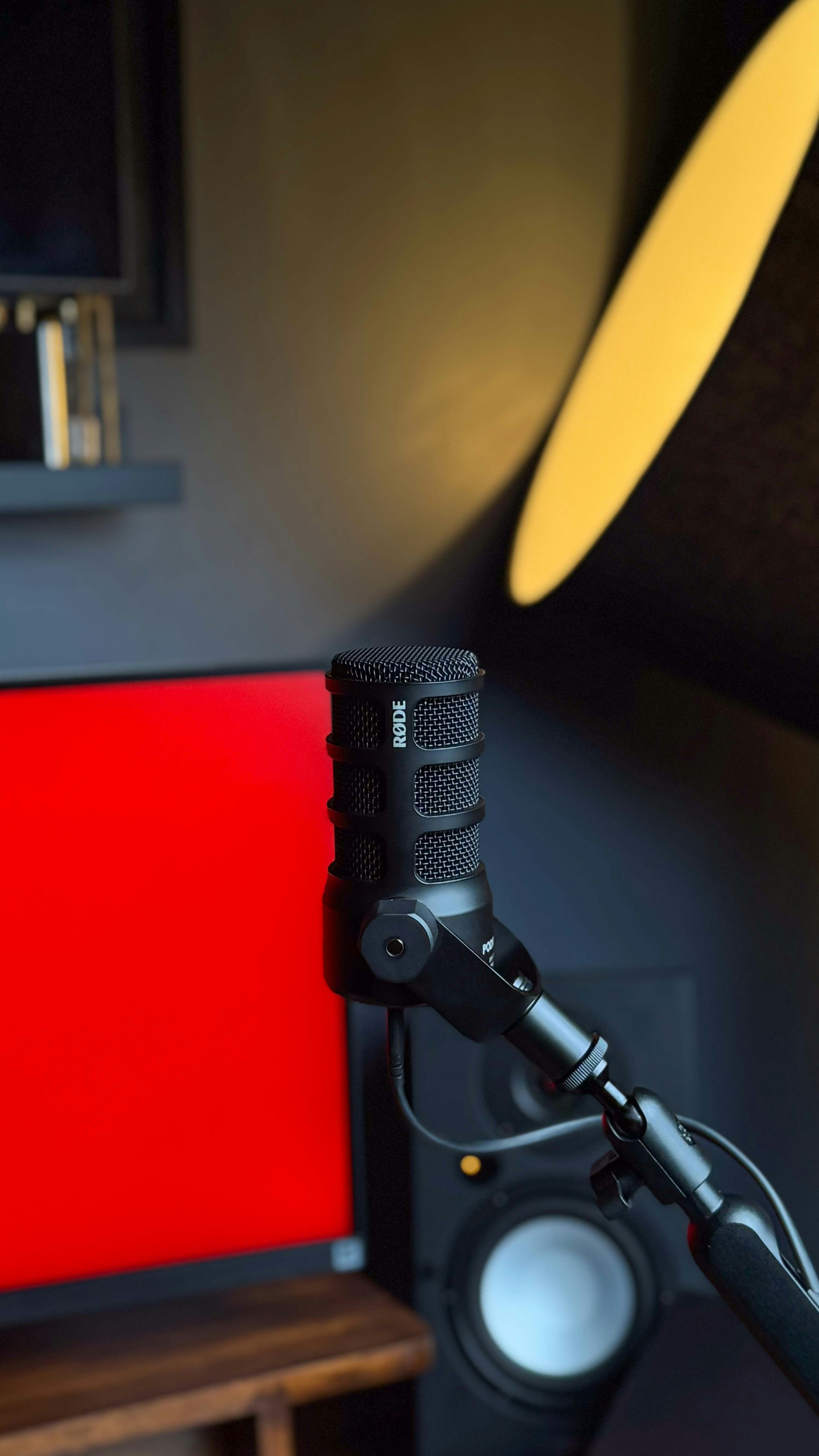 Black Rode microphone positioned prominently in a modern recording studio, with a vibrant red backdrop and soft lighting creating a dynamic atmosphere.