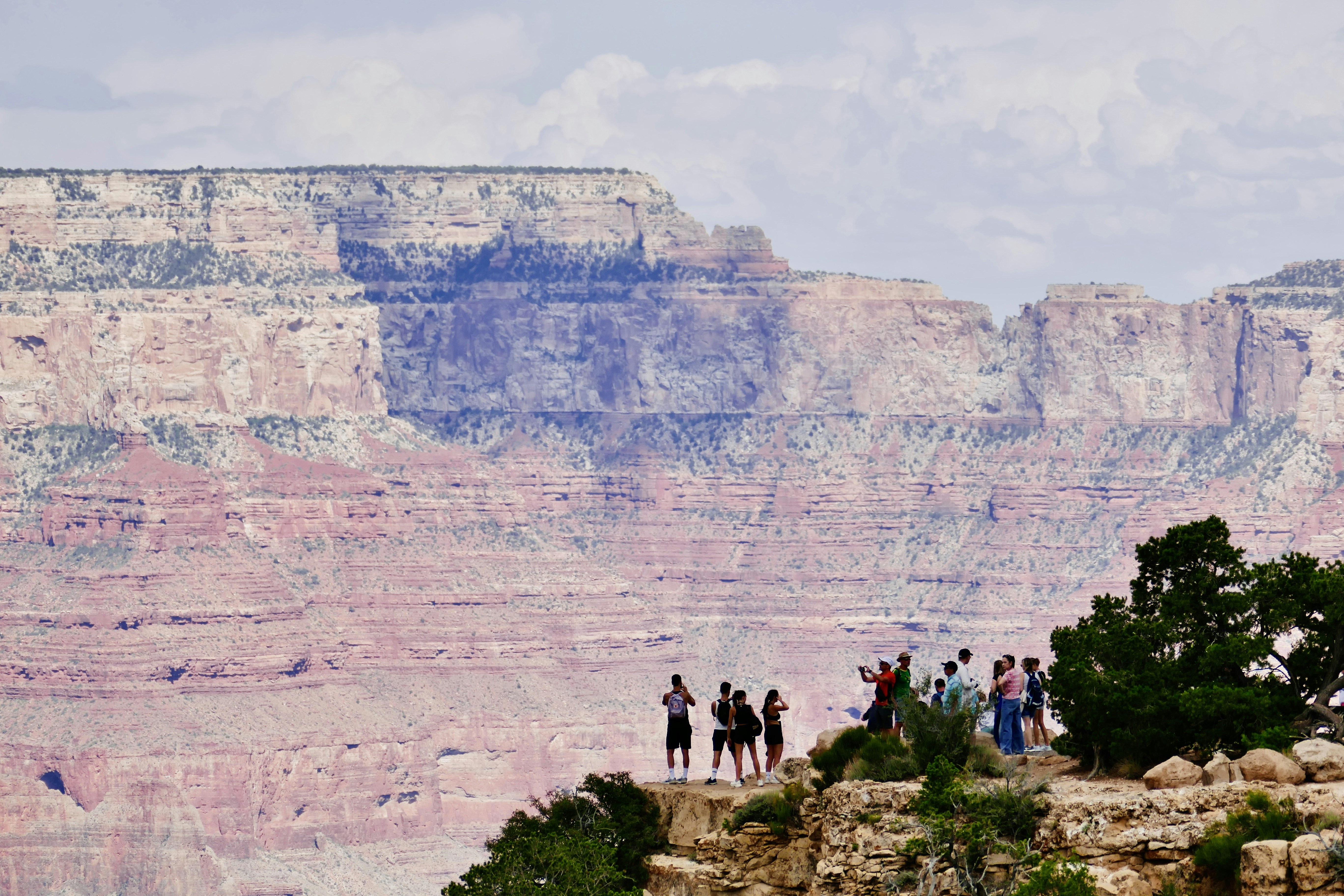 Hikers stand along a canyon rim with layered cliffs receding in the distance, capturing a panoramic Grand Canyon overlook.