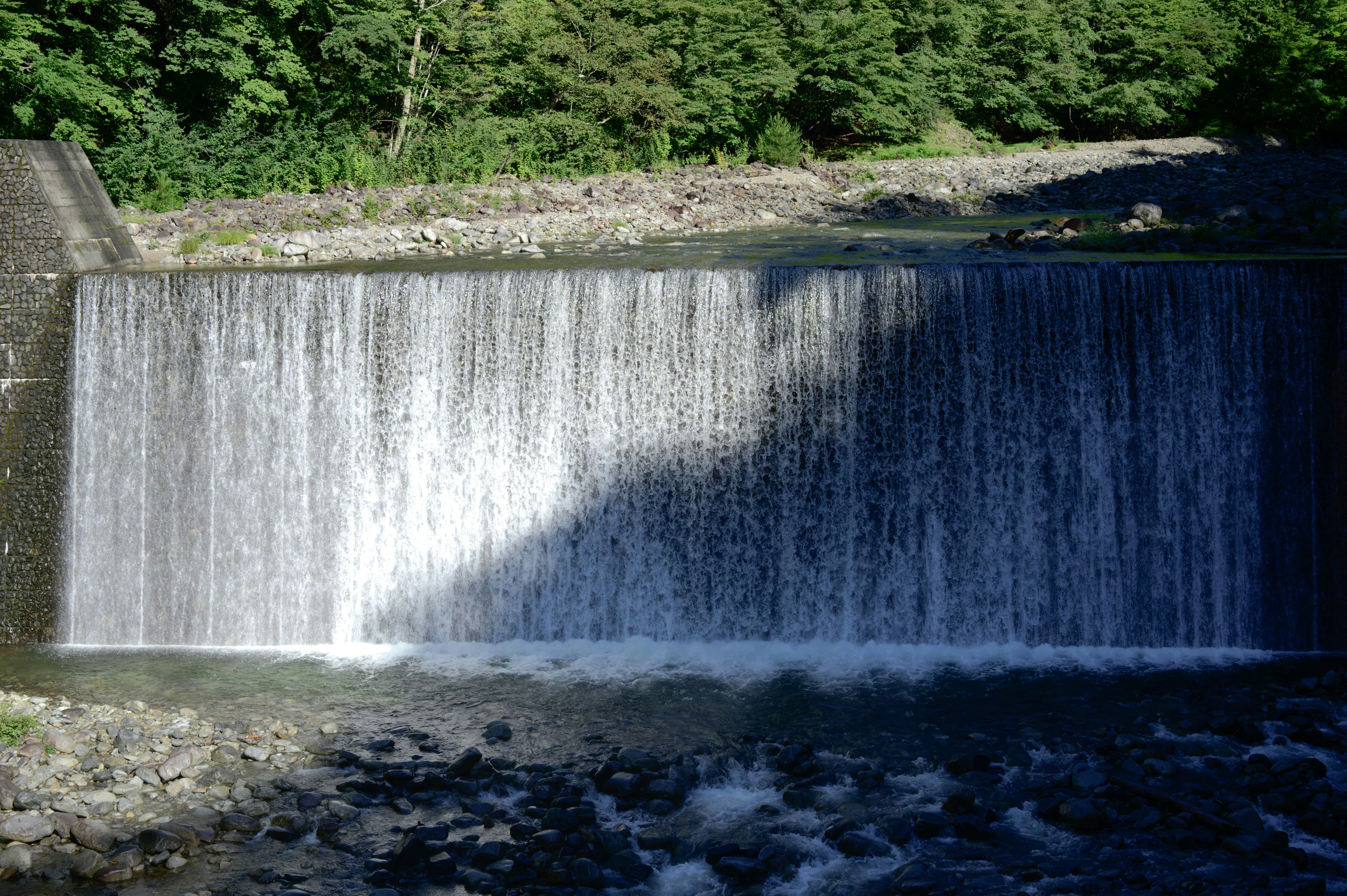 Veiled Cascade Over a Concrete Spillway in Dappled Forest Light