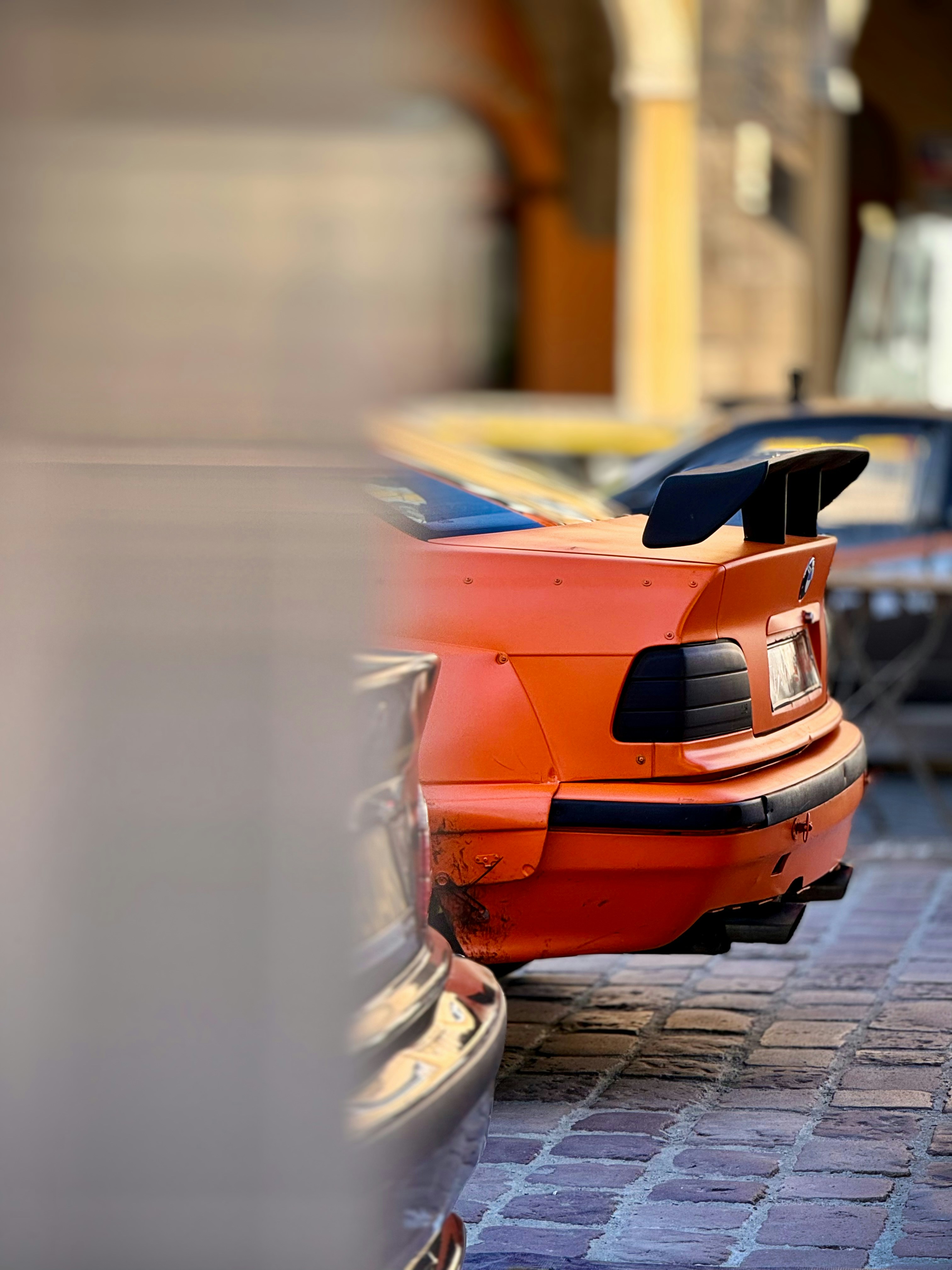 Tail-end of an orange sports car peeking from a cobbled street