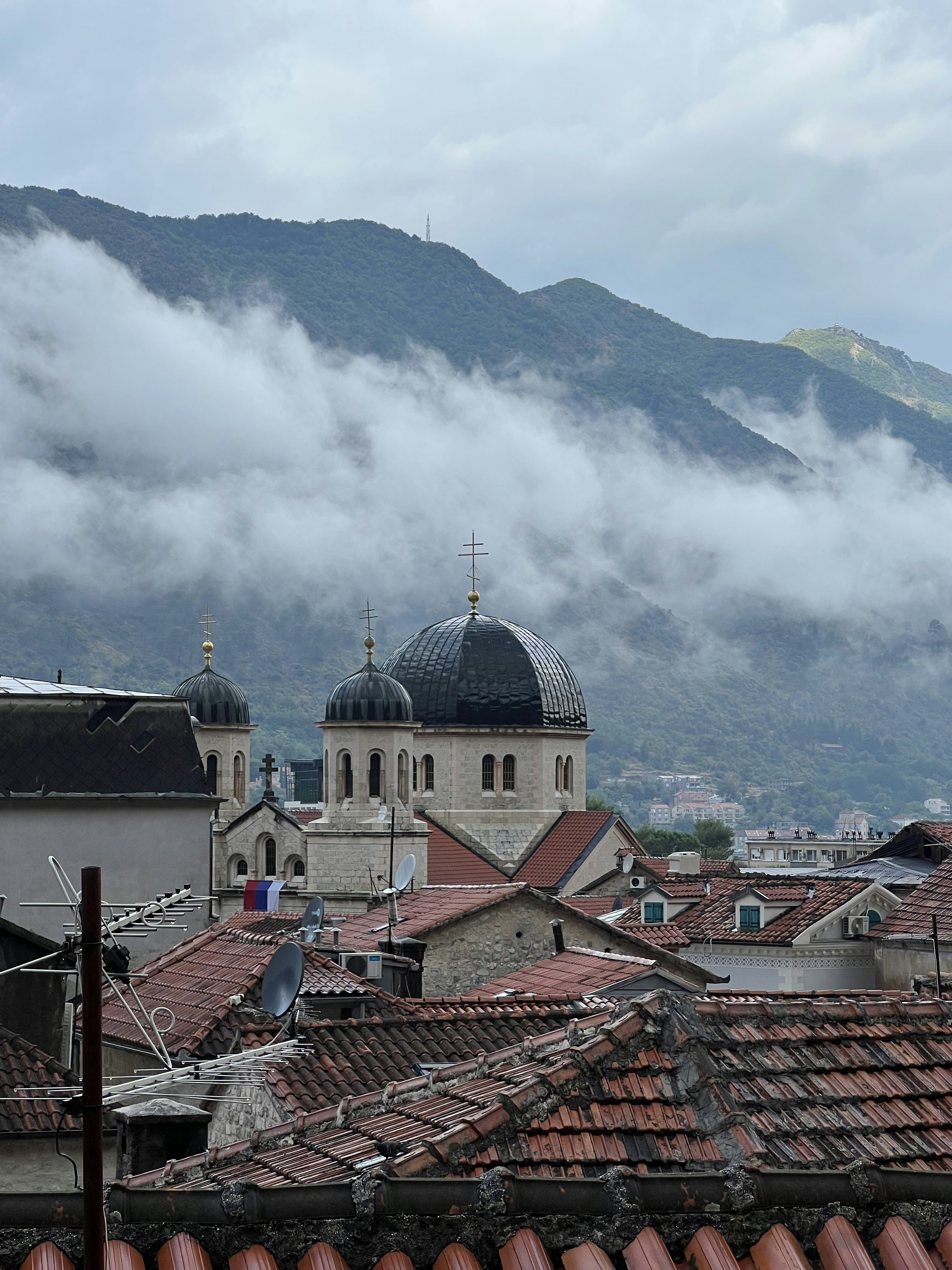 Dome-Top Cathedral Over Red Rooftops Beneath a Cloud-Kissed Alpine Sky