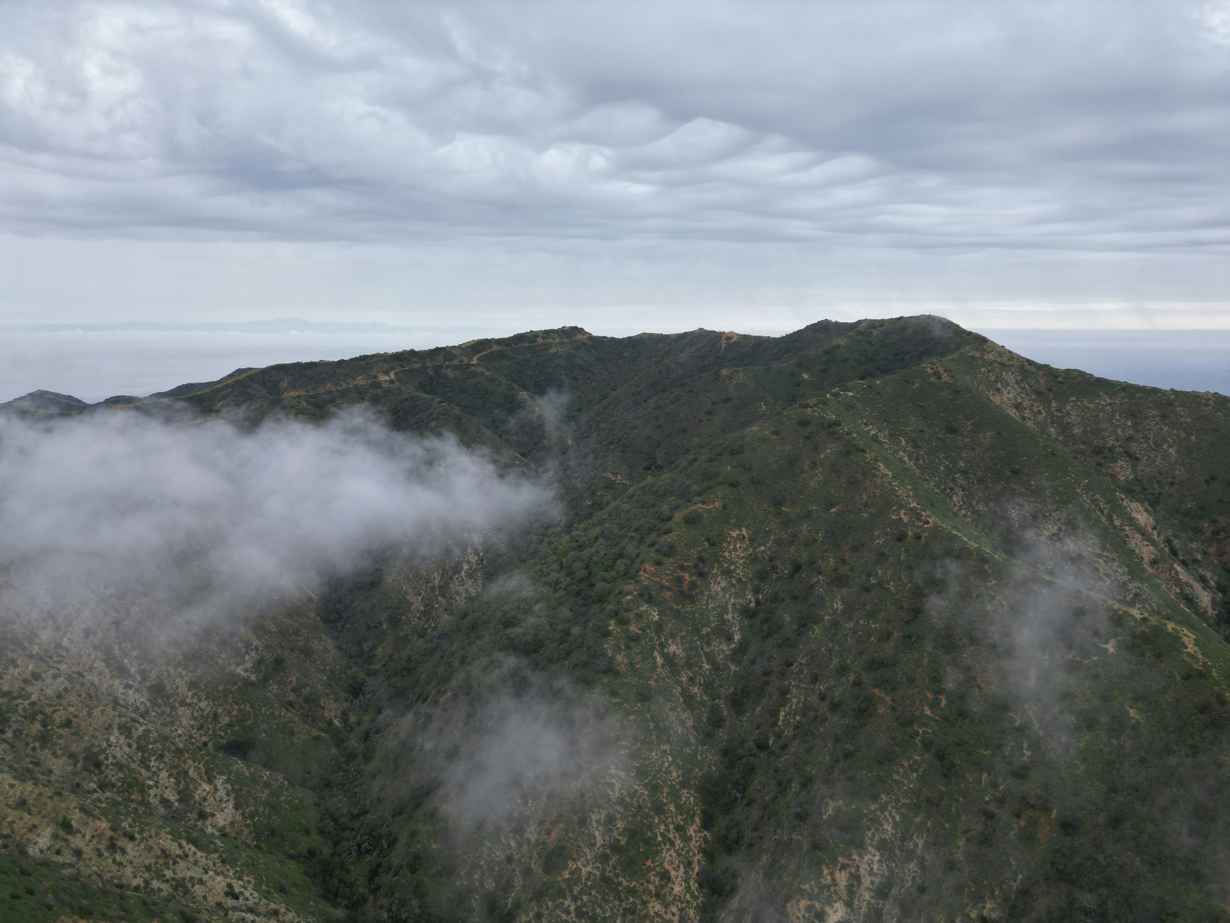 Mountain ridges partially obscured by low-hanging clouds under a textured sky.
