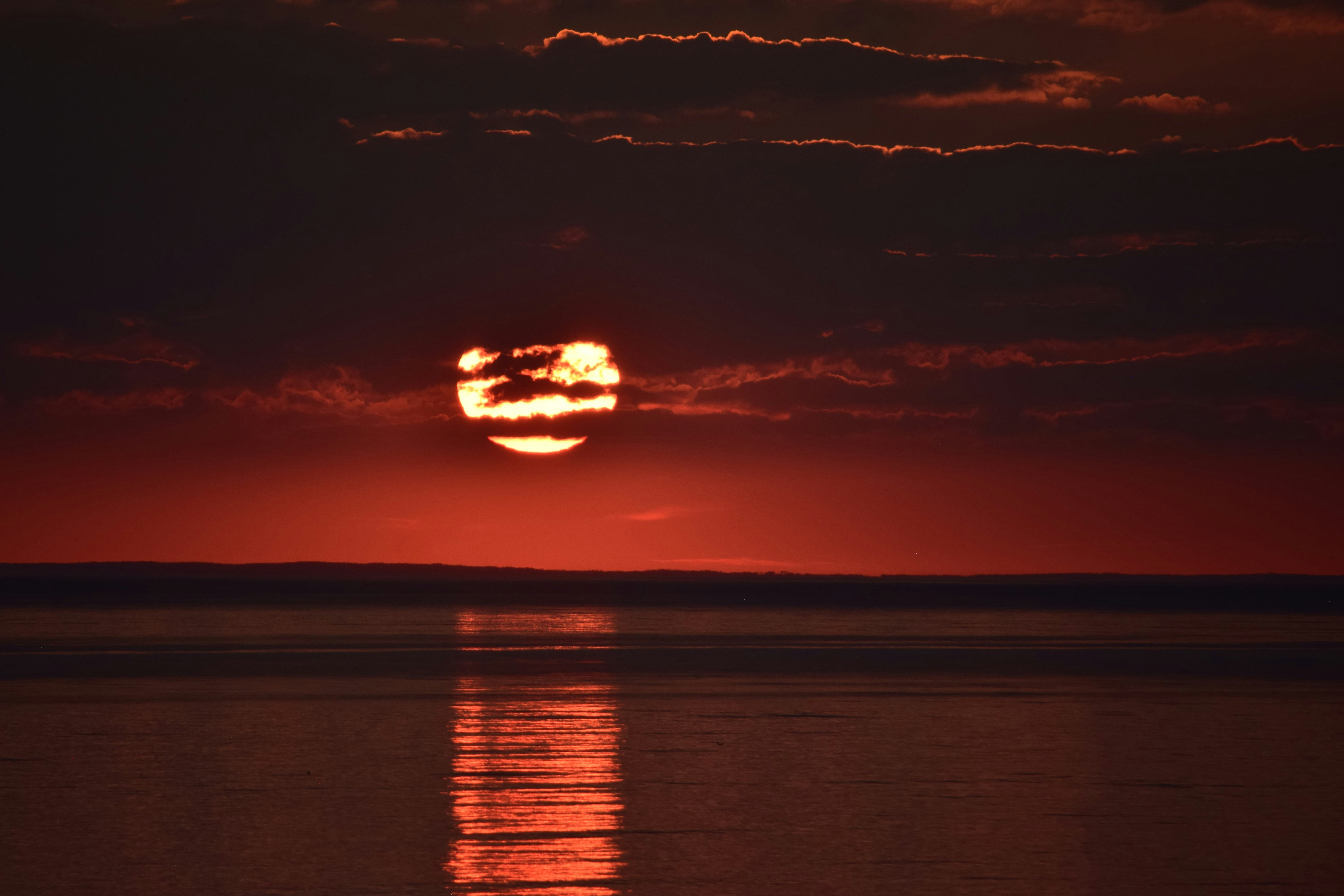 Crimson Sun Halved by Clouds Over a Quiet Horizon