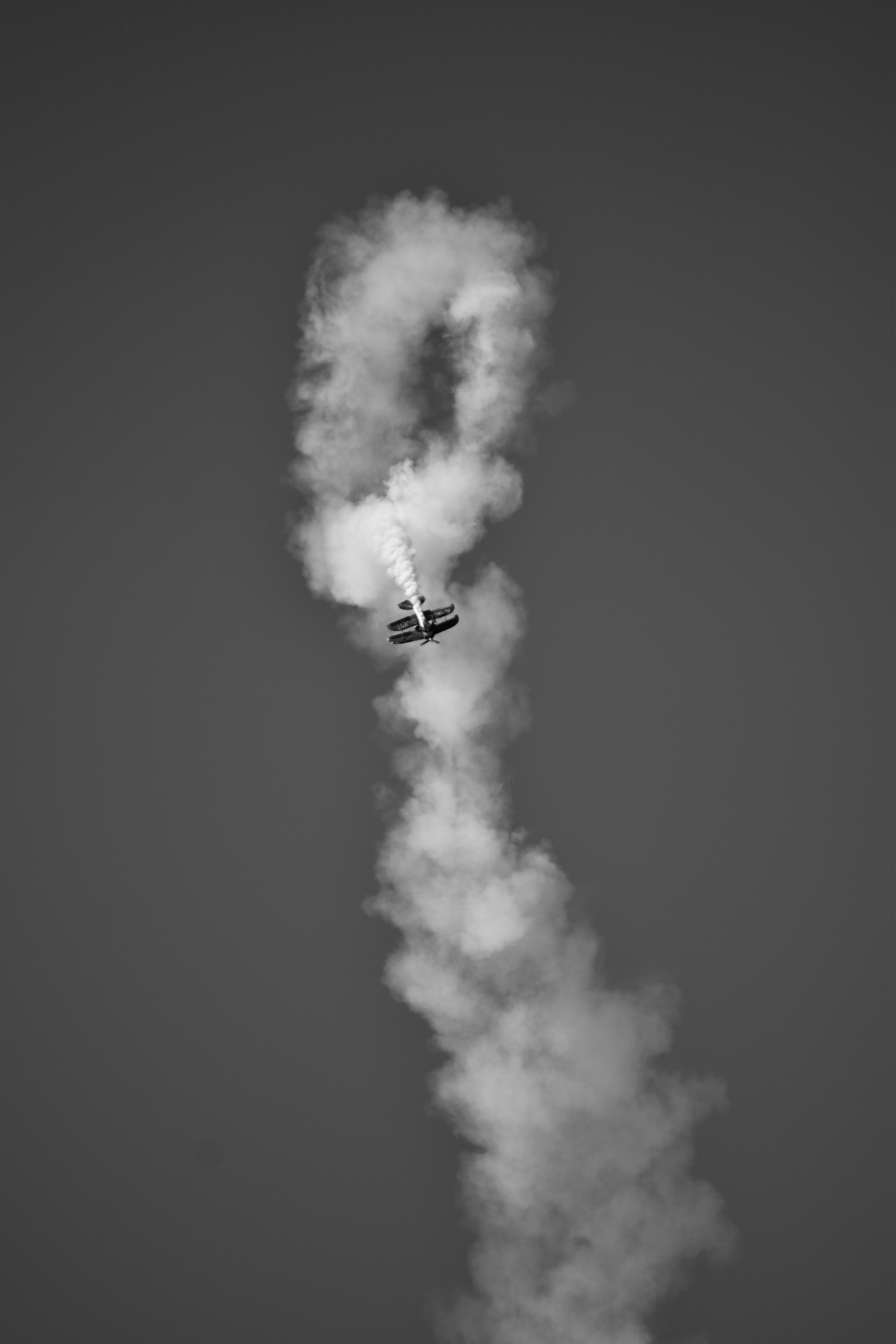 Vertical Spiral: A Biplane Traces a Smoke Ribbon in a Narrow Sky