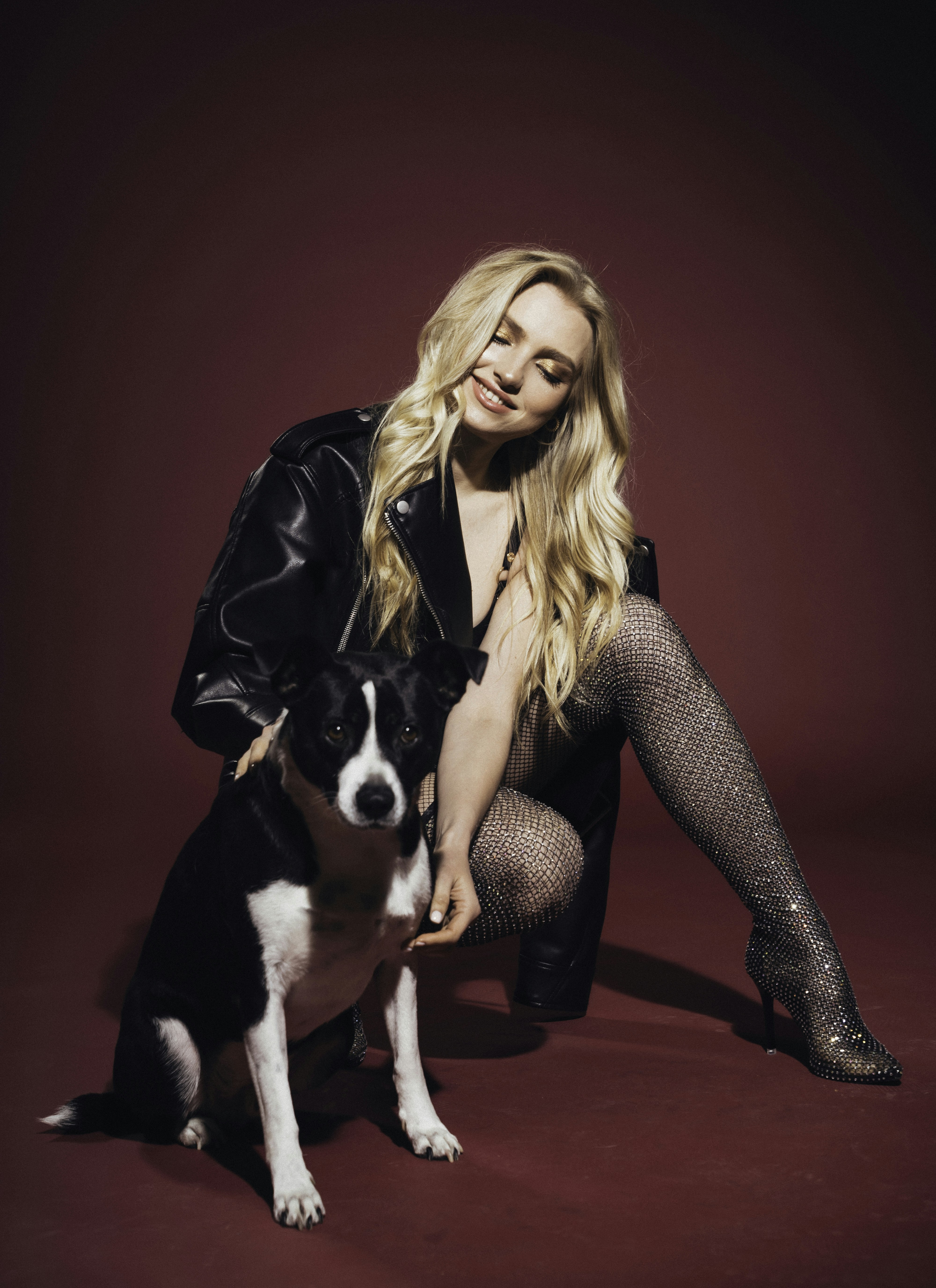 Crimson Studio Portrait: Leather-Clad Blonde and Her Black‑and‑White Dog