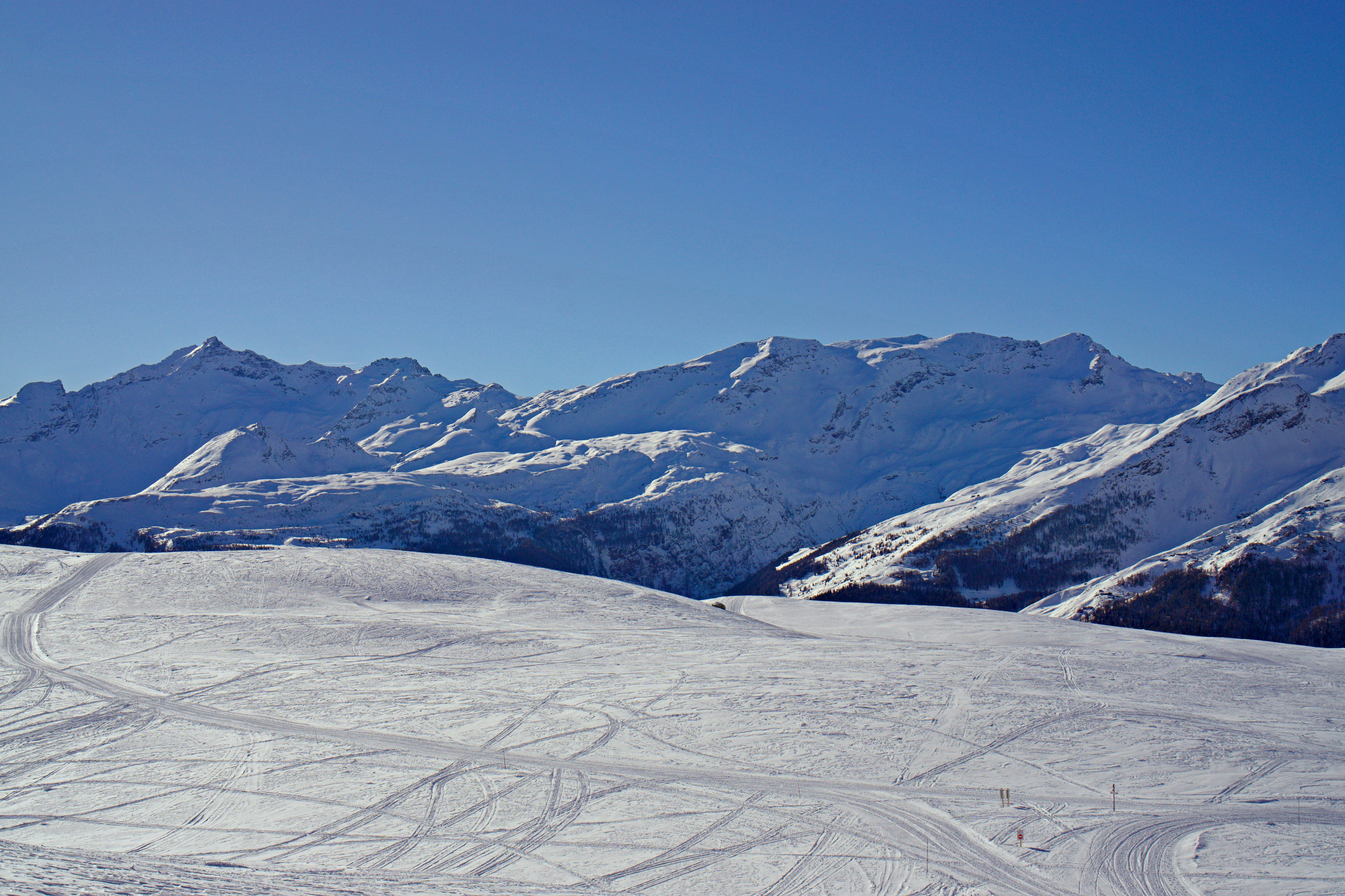 Skier gracefully descending a sunlit snowy slope with majestic mountain range in the background.