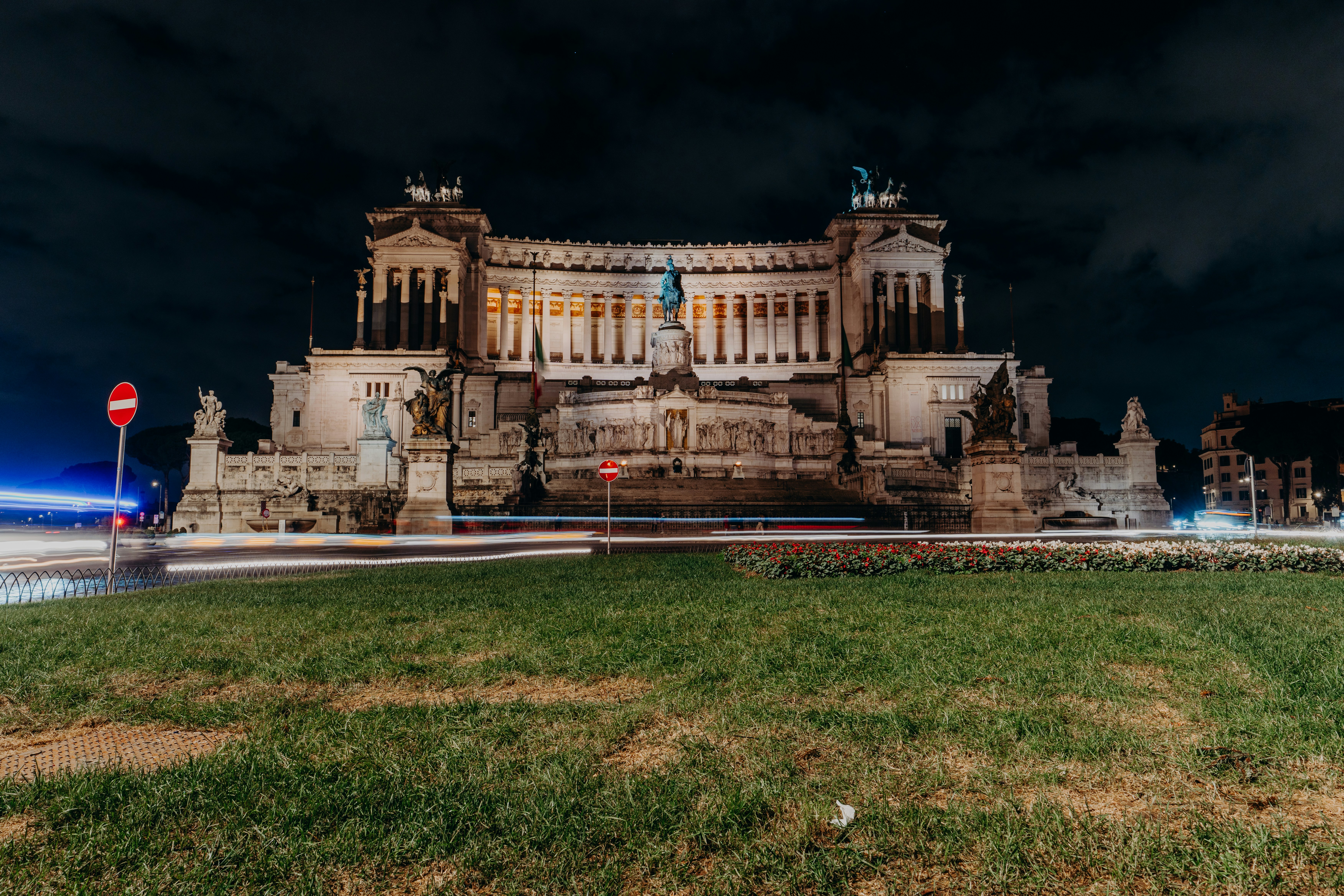 Historic building illuminated against a dark sky with streaks of light from passing vehicles.