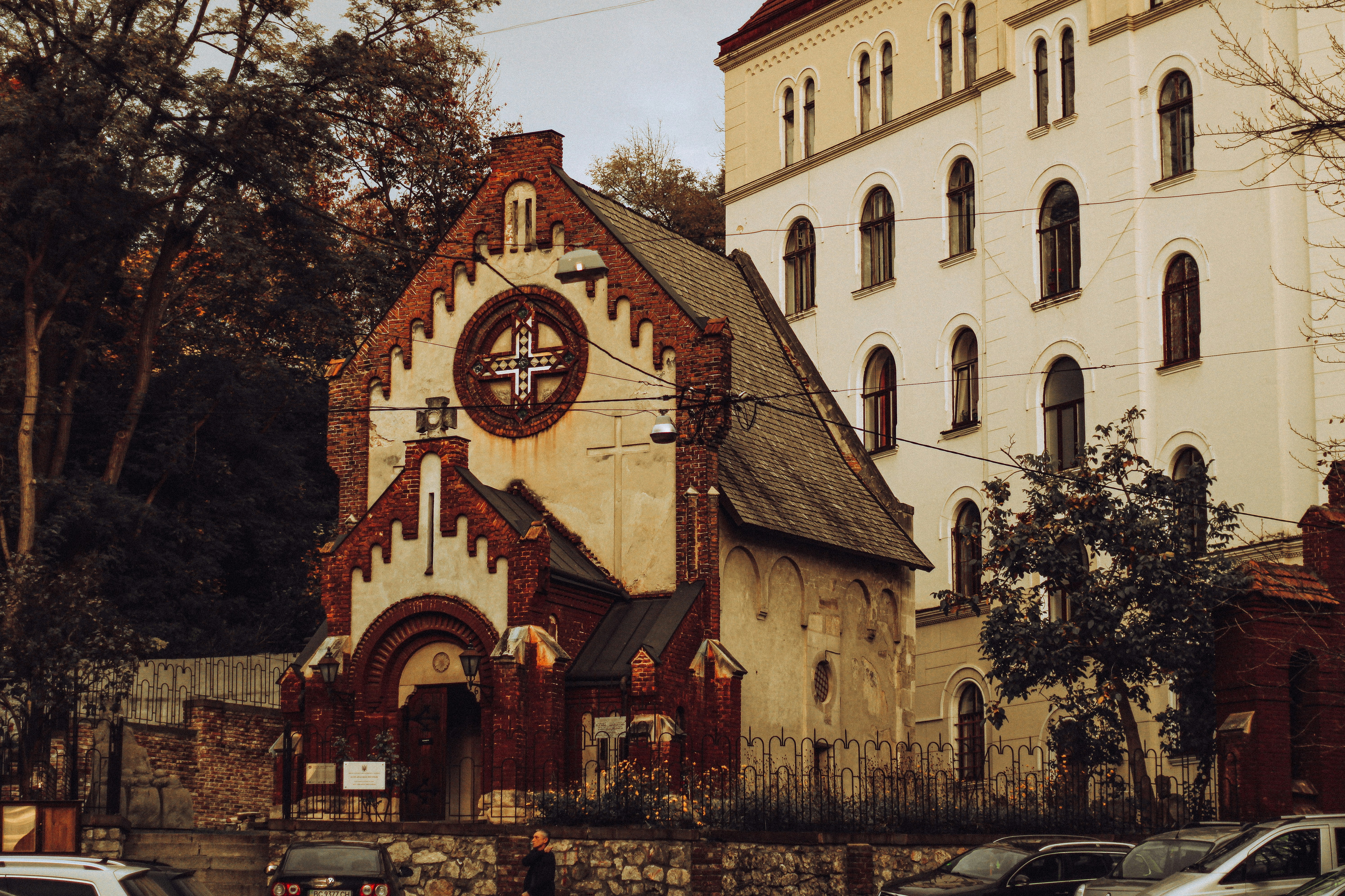 A quaint brick church with a distinctive cross design nestled among modern buildings, showcasing a blend of historical and contemporary architecture.
