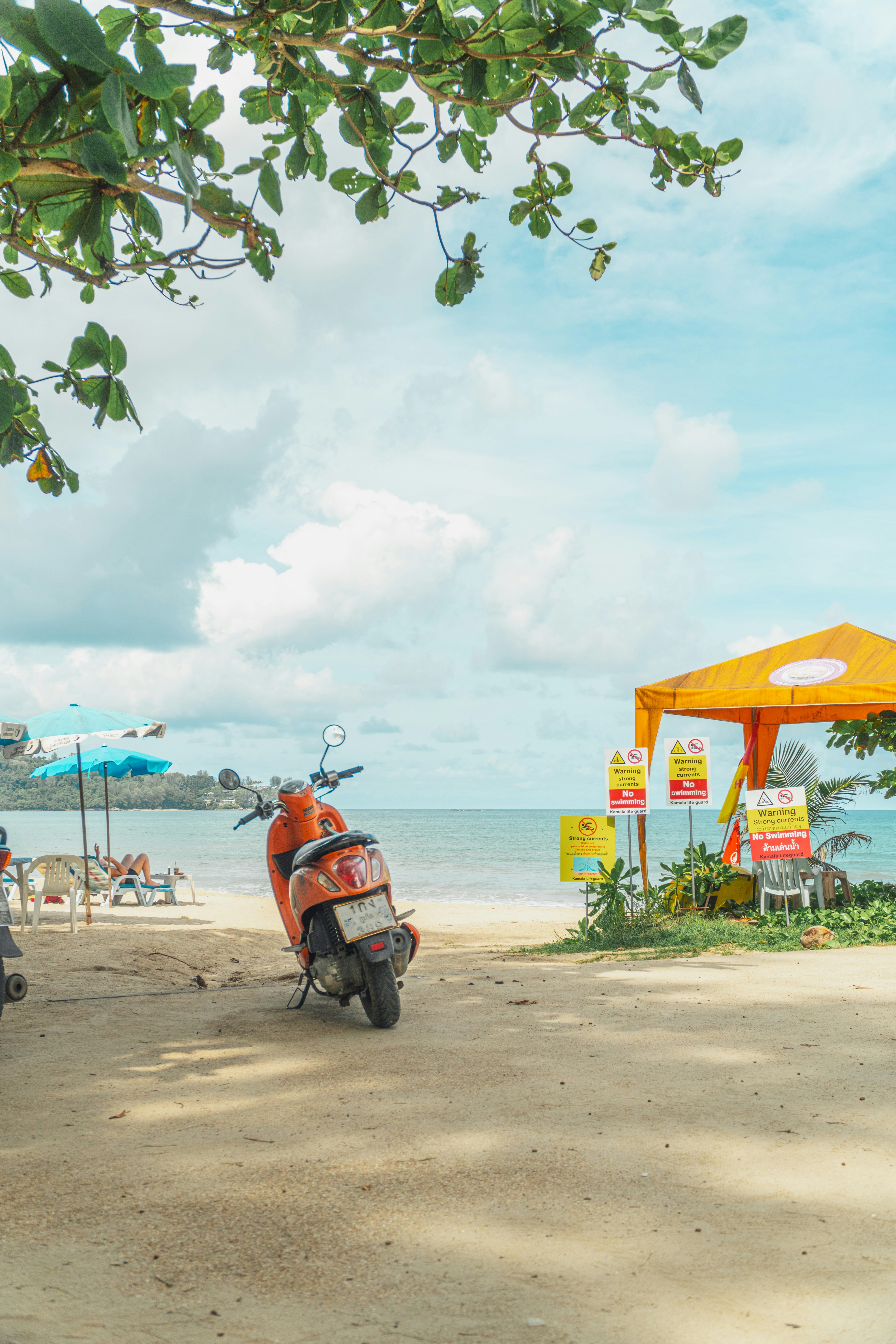 Sunlit Beach Scooter: Orange Ride Nestled Under a Leafy Canopy and Coastal Tent