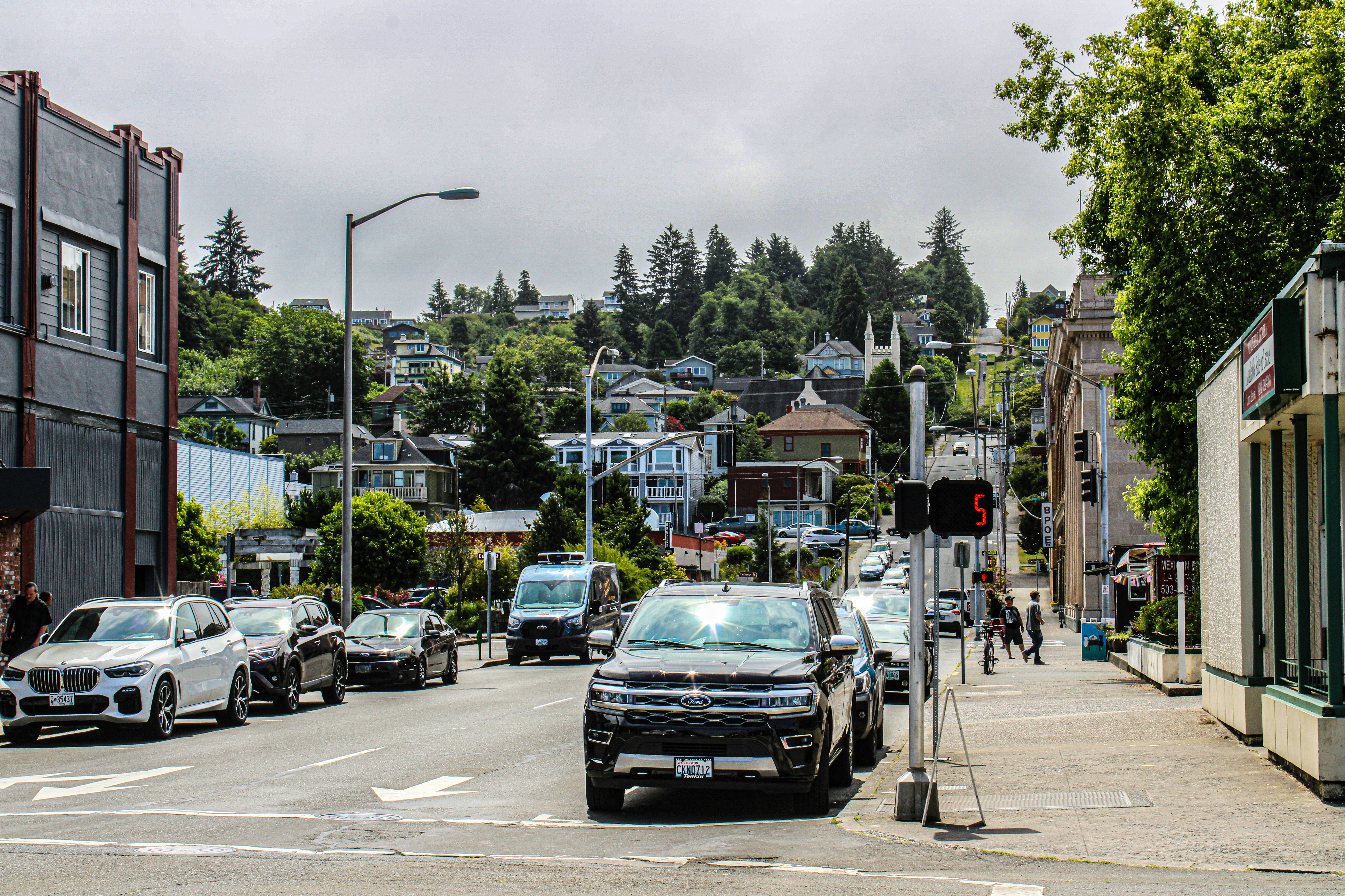 Center Lane, Quiet Traffic: A Black SUV Anchors a Suburban Street Beneath Hillside Homes