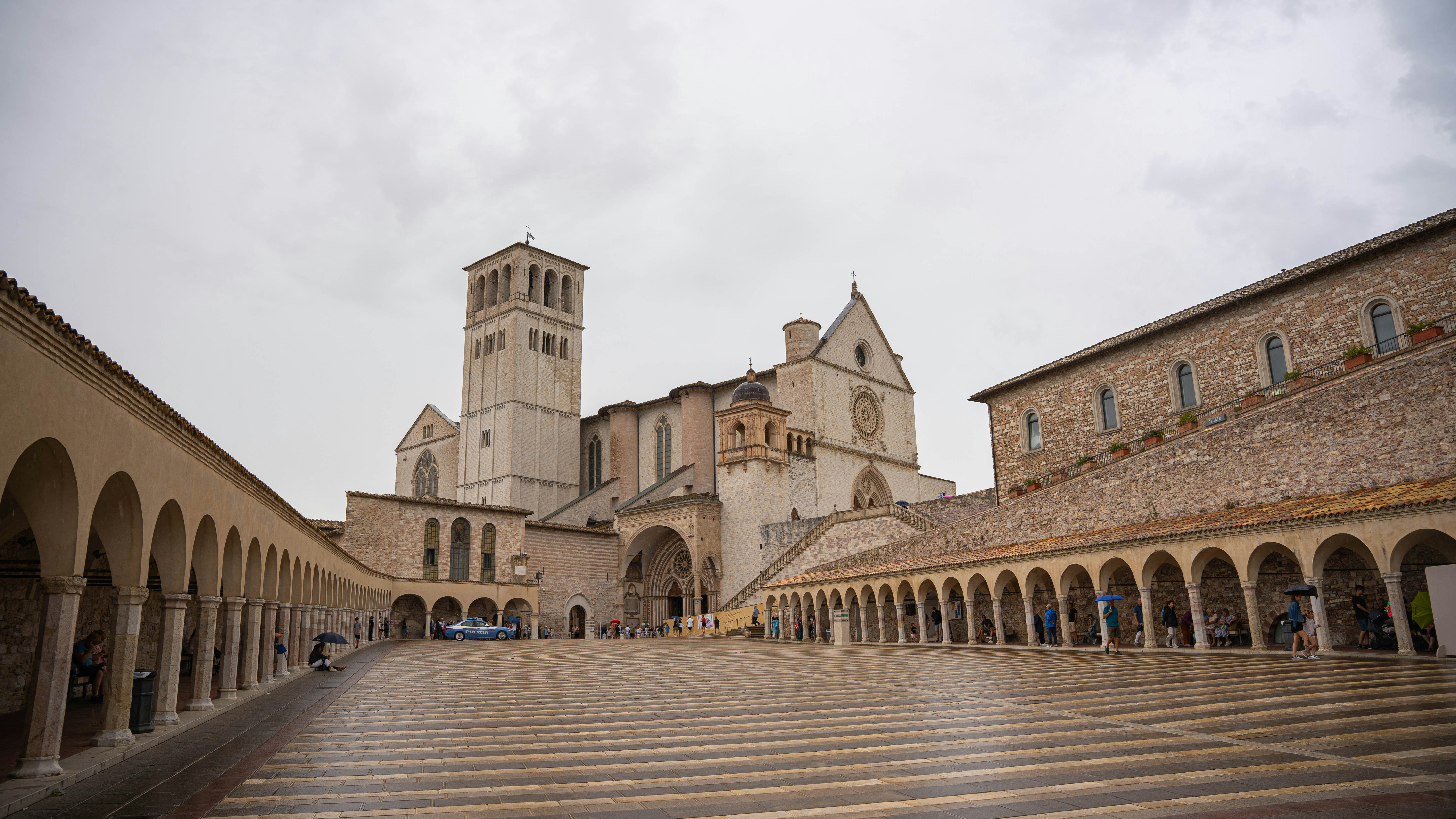 Historic basilica with expansive stone courtyard and towering arches under a cloudy sky.