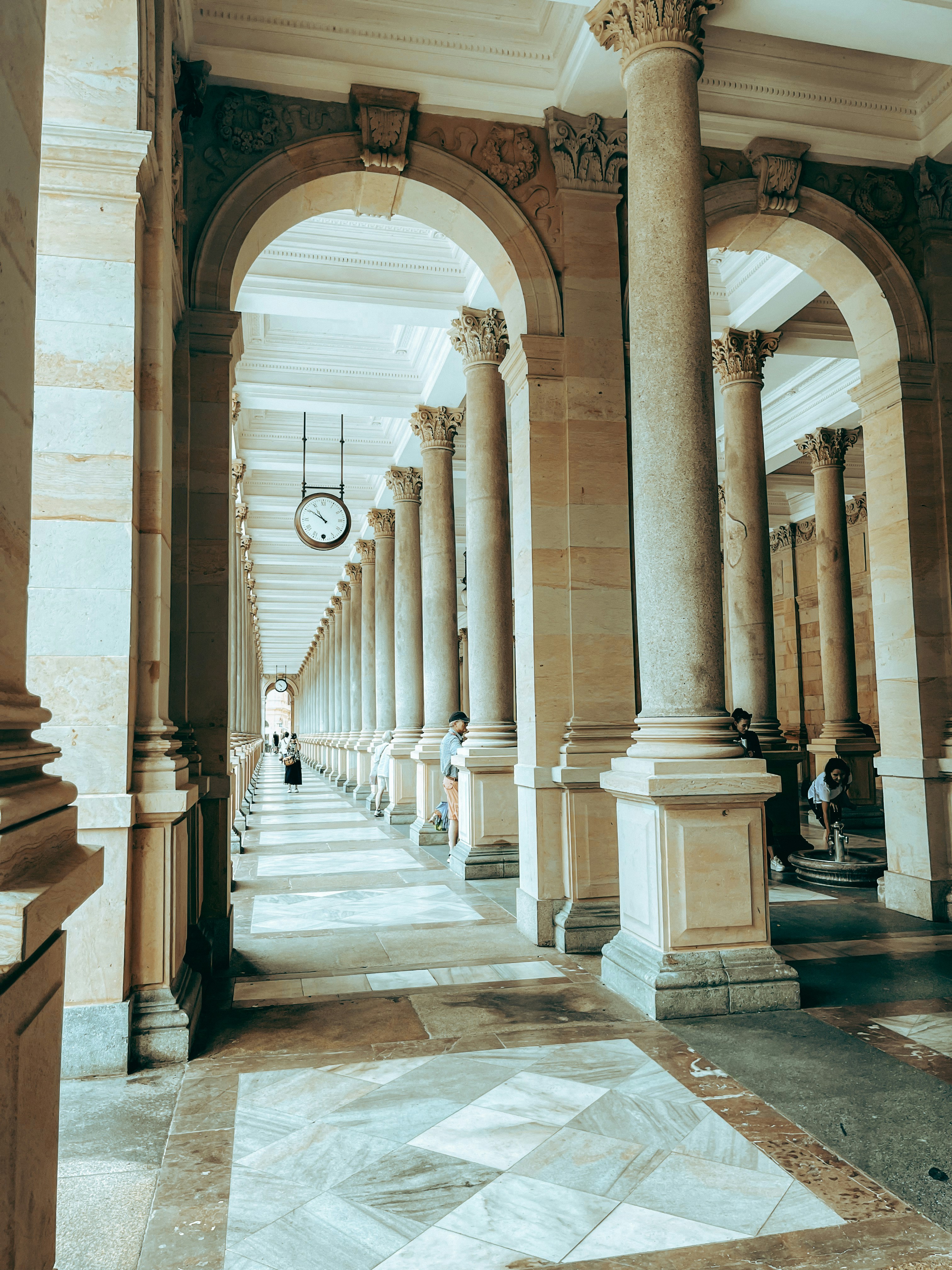 A long hallway with columns and a clock on the wall photo – Free Mill ...