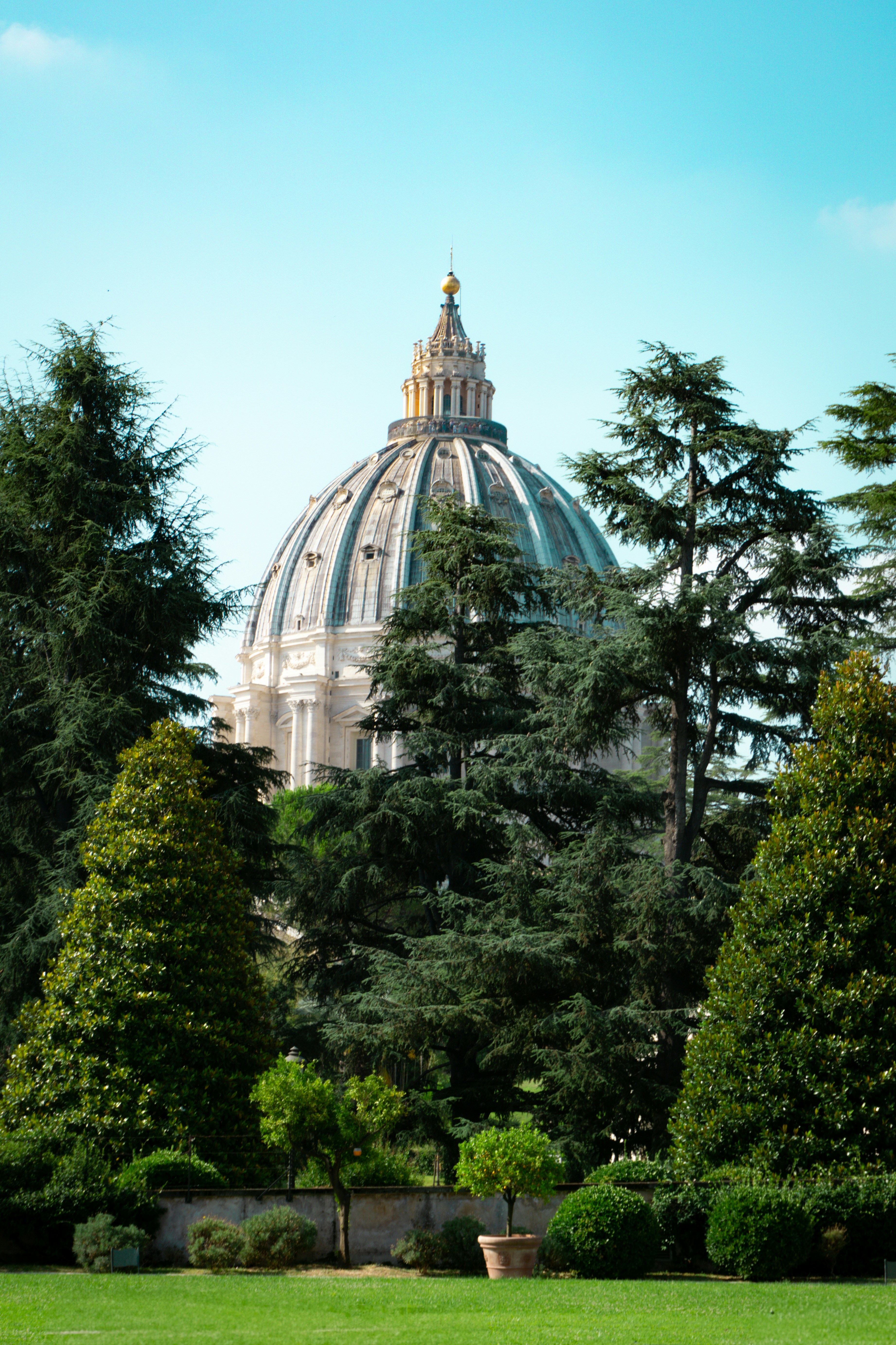 A serene view of the dome of St. Peter's Basilica peeking through the lush greenery of the Vatican Gardens in Rome. The contrast between the architectural splendor of the dome and the vibrant natural surroundings creates a peaceful and harmonious scene. The well-maintained garden adds to the tranquil atmosphere, making this an idyllic spot within Vatican City.