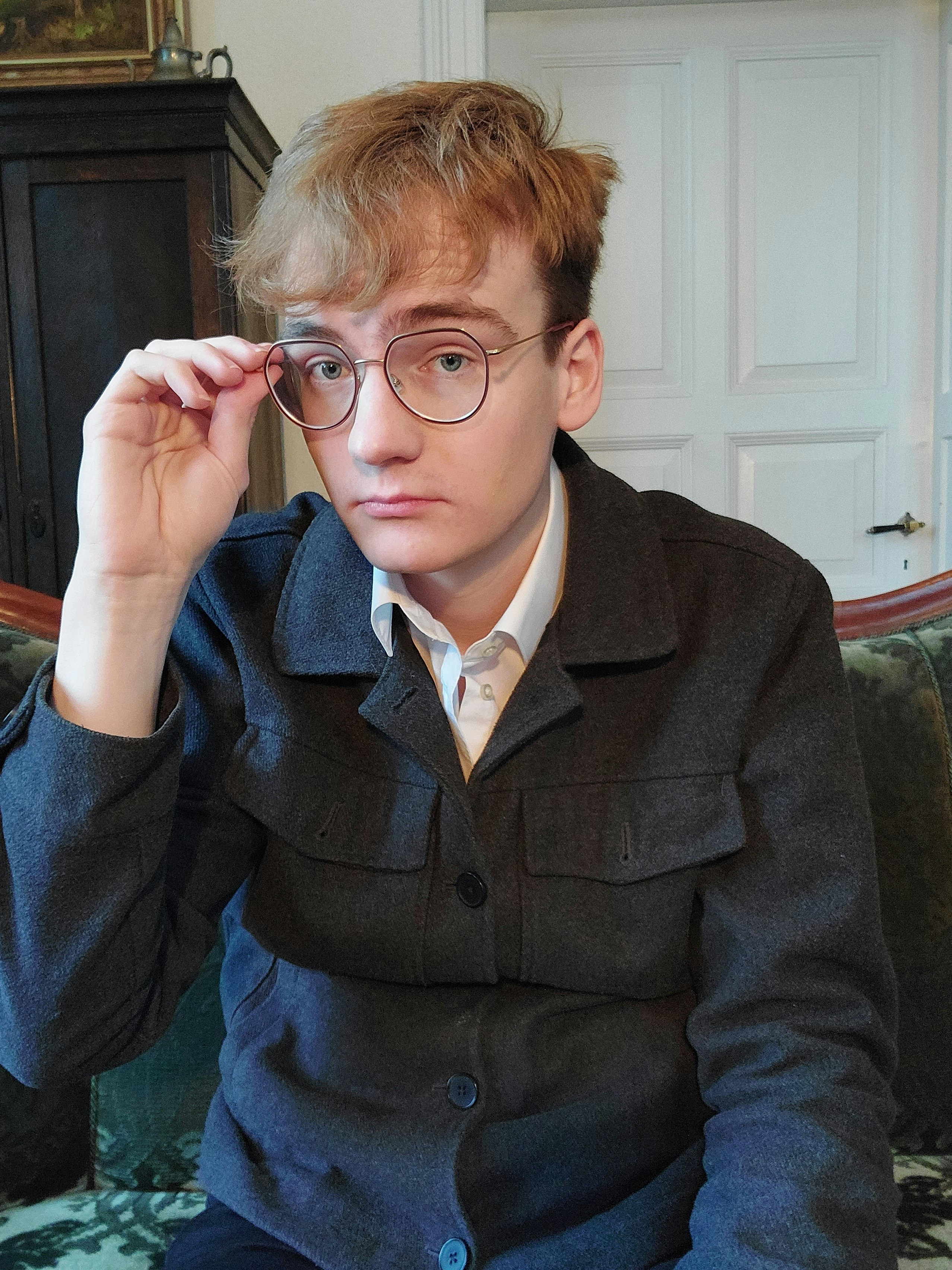 Contemplative Gaze in a Vintage Room: Glasses and a Dark Wool Jacket under Soft Indoor Light