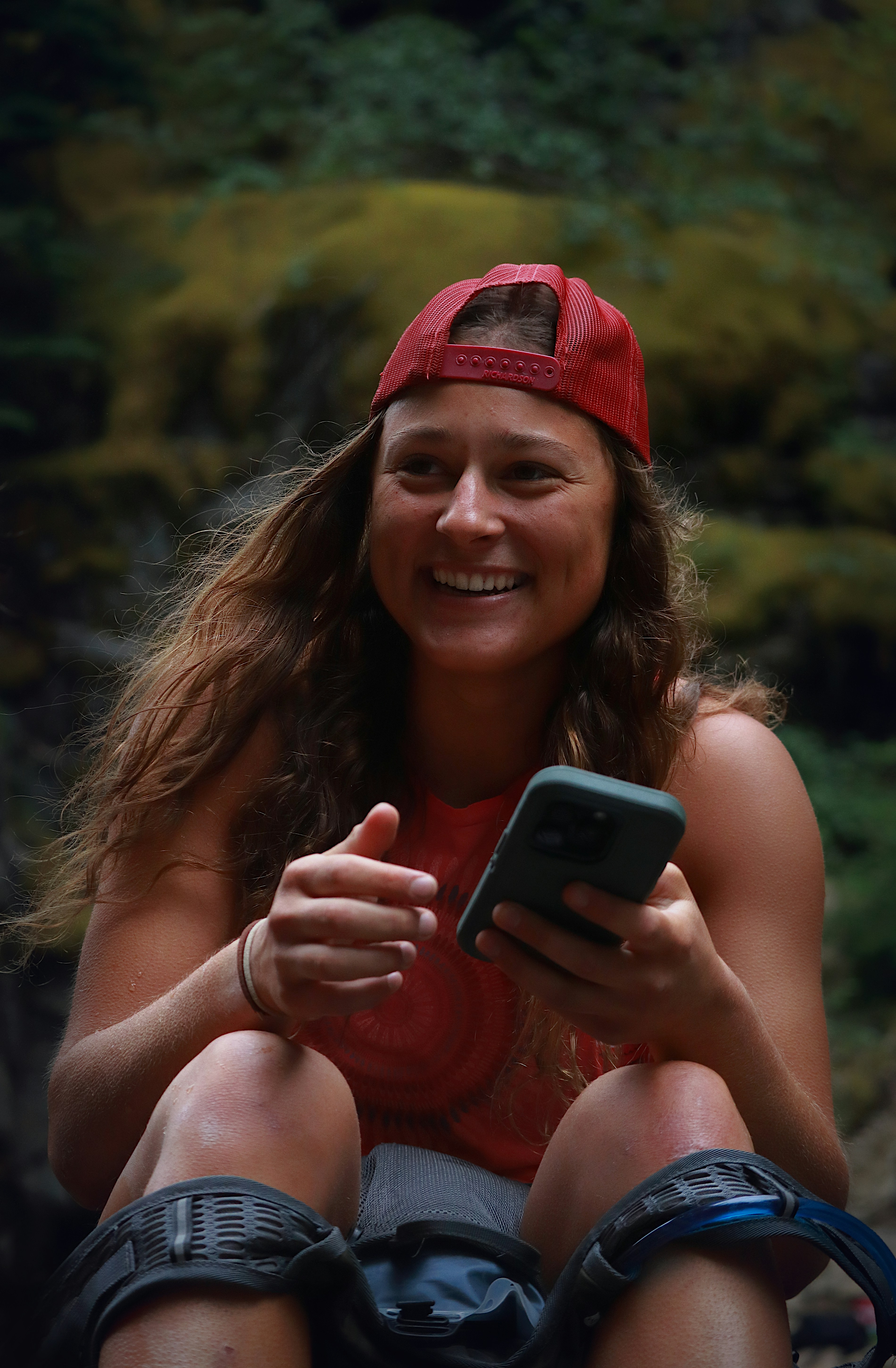 Smiling Adventurer in a Red Cap Shares a Moment with a Phone