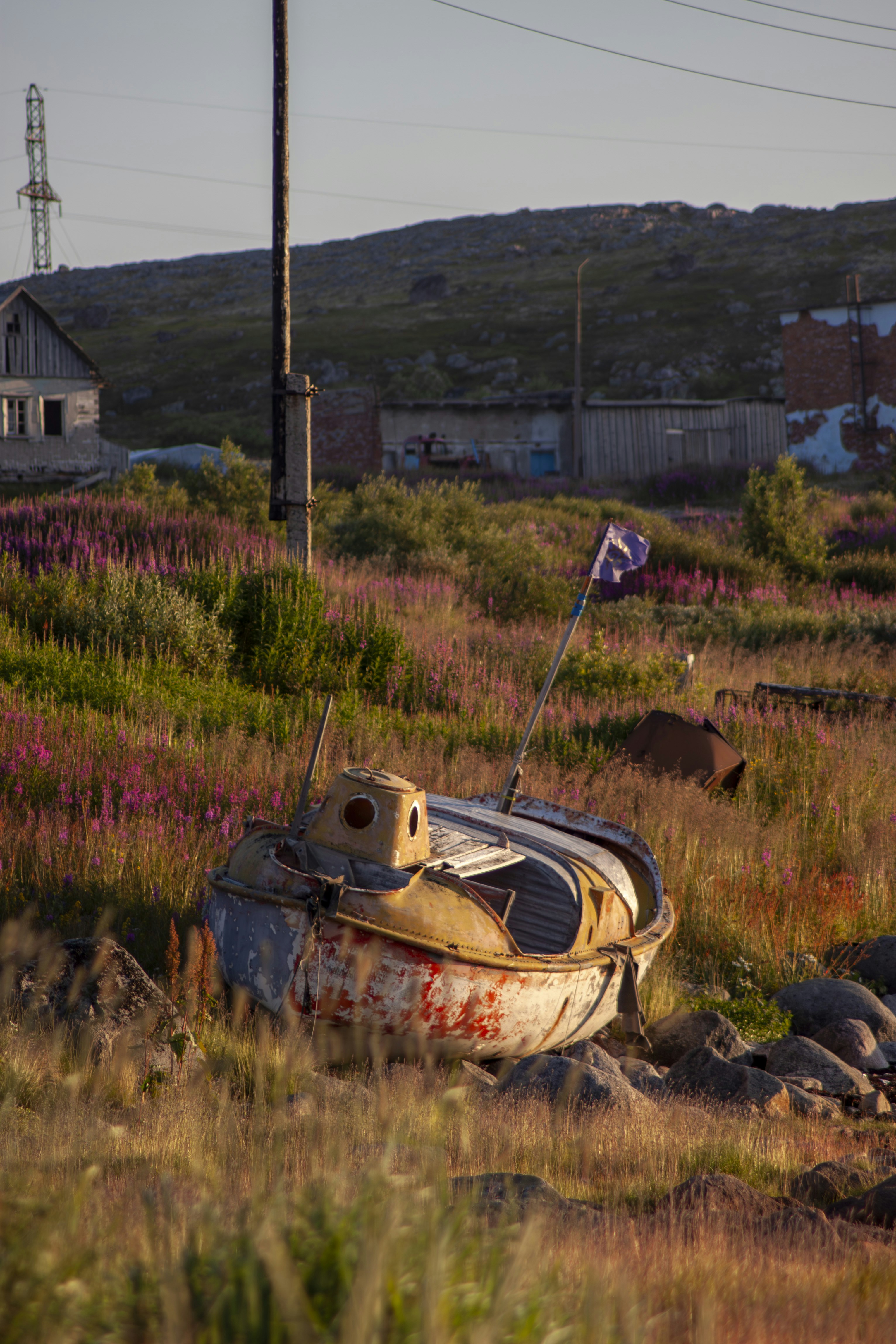 Weathered Boat in a Purple Field: Quiet Decay Beneath a Distant Industrial Skyline