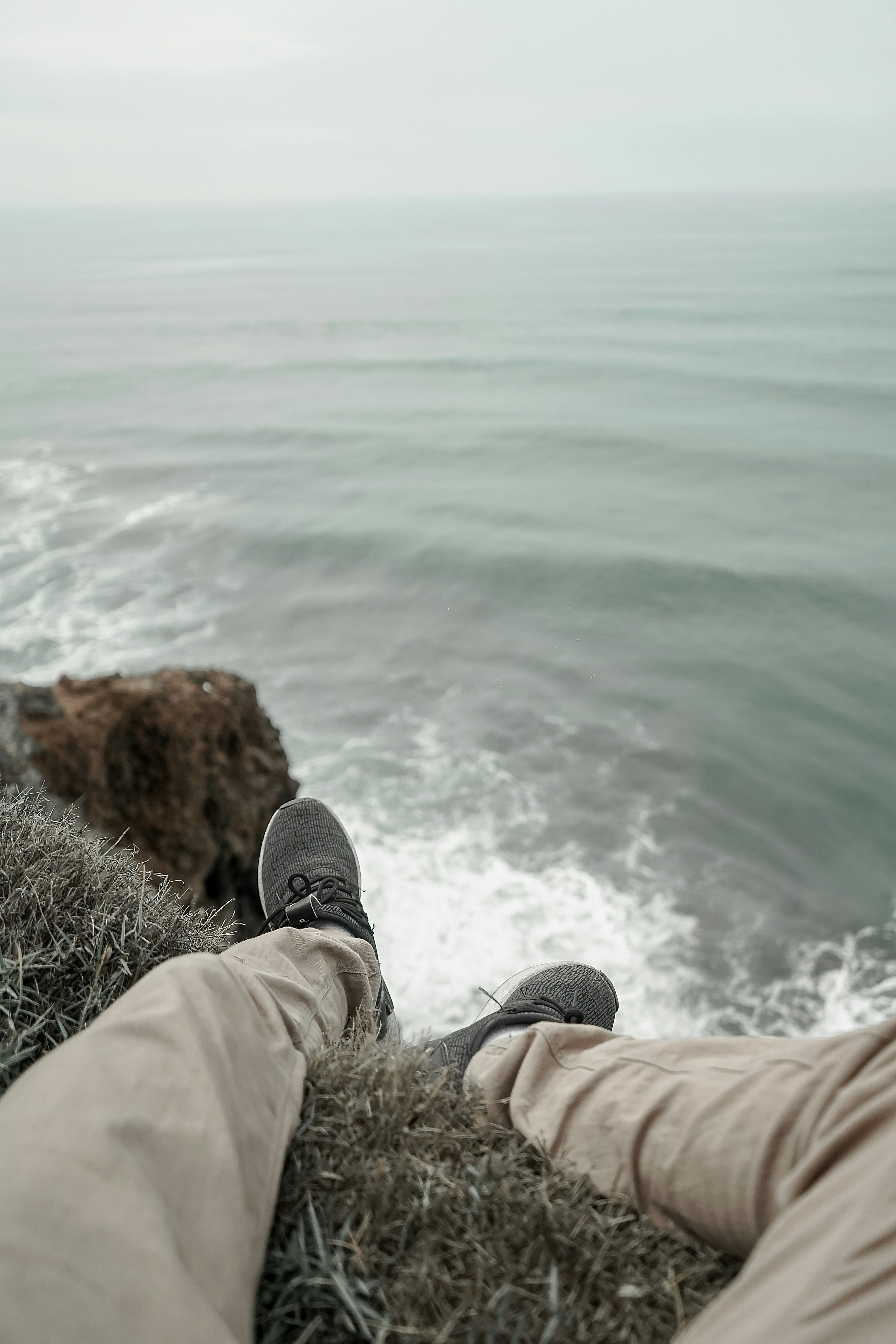 A person laying on top of a cliff next to the ocean photo – Free ...