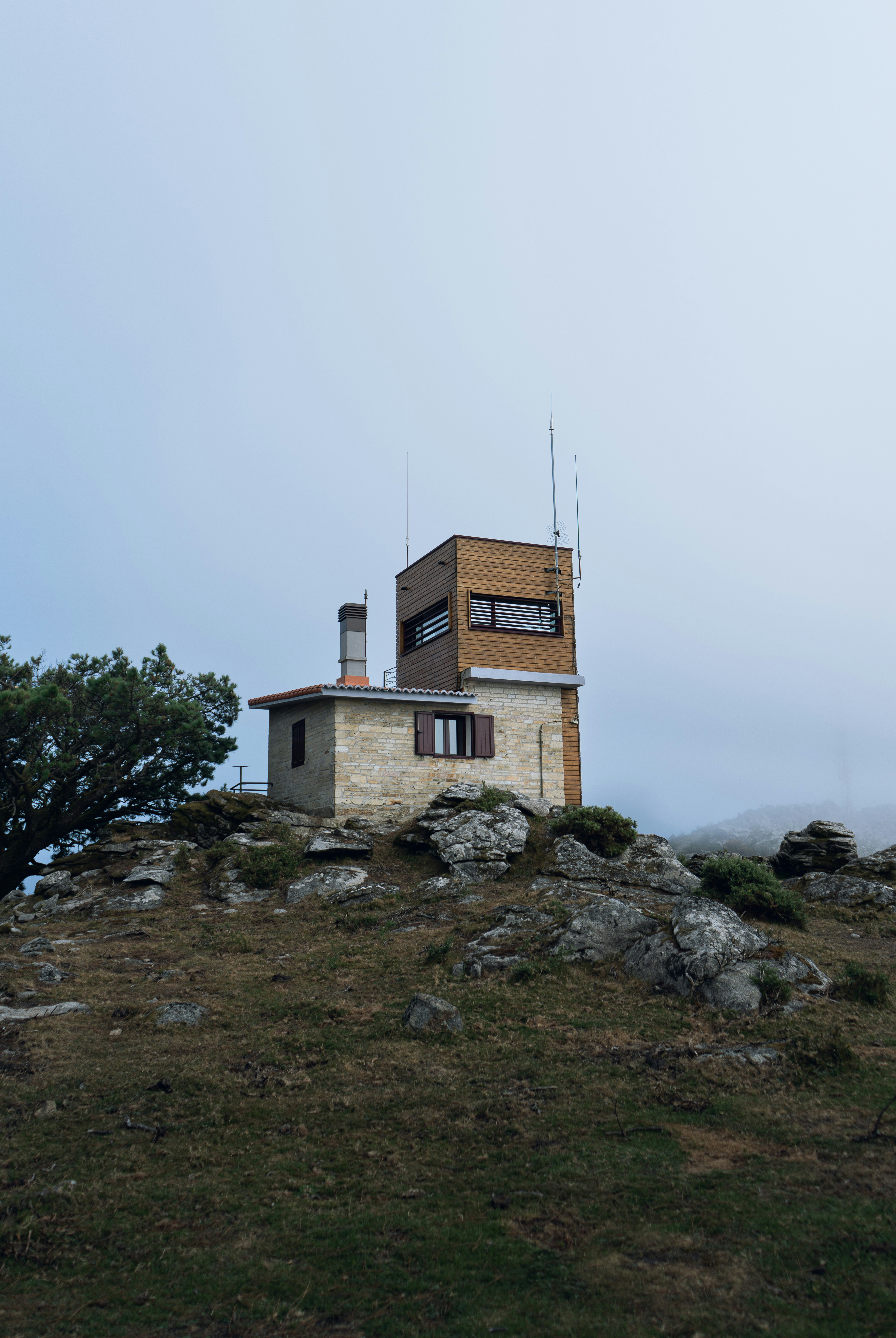 Ridge Sentinel: Stone House with a Wooden Tower Beneath a Misty Blue Sky