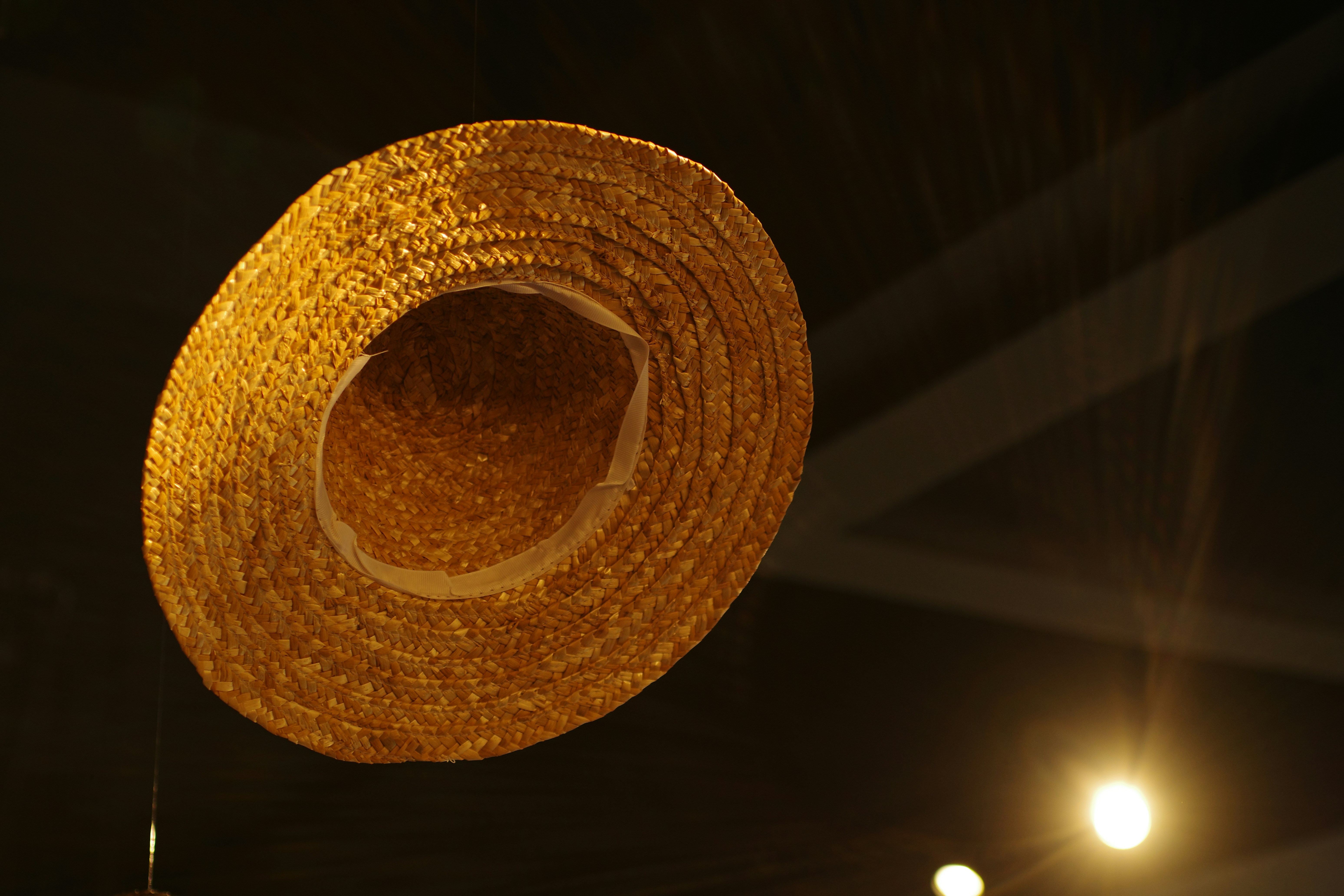 A straw hat hanging from a ceiling in a dark room photo – Free Hat ...