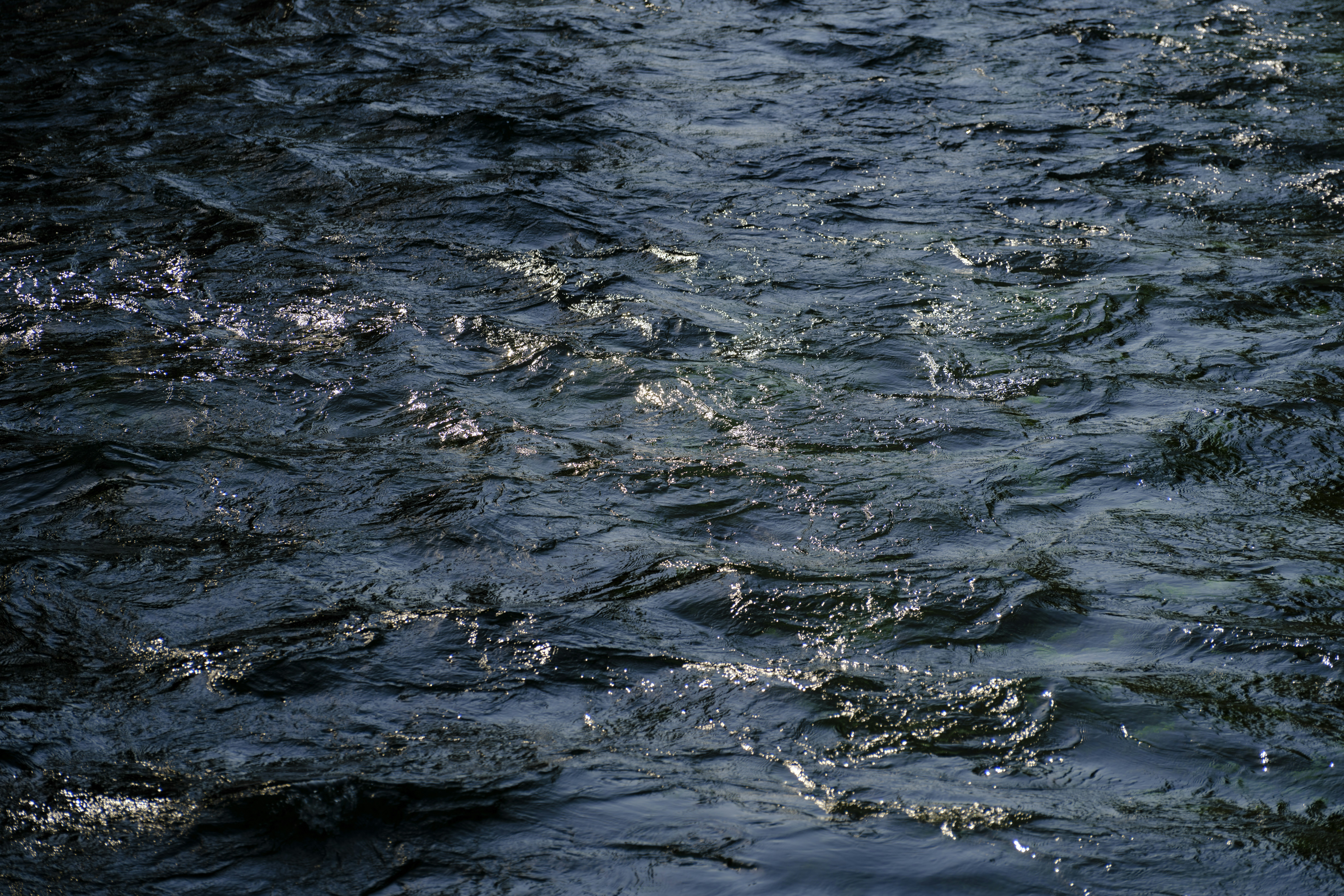Gentle ripples on a dark water surface, illuminated by soft light, creating a serene and tranquil atmosphere.