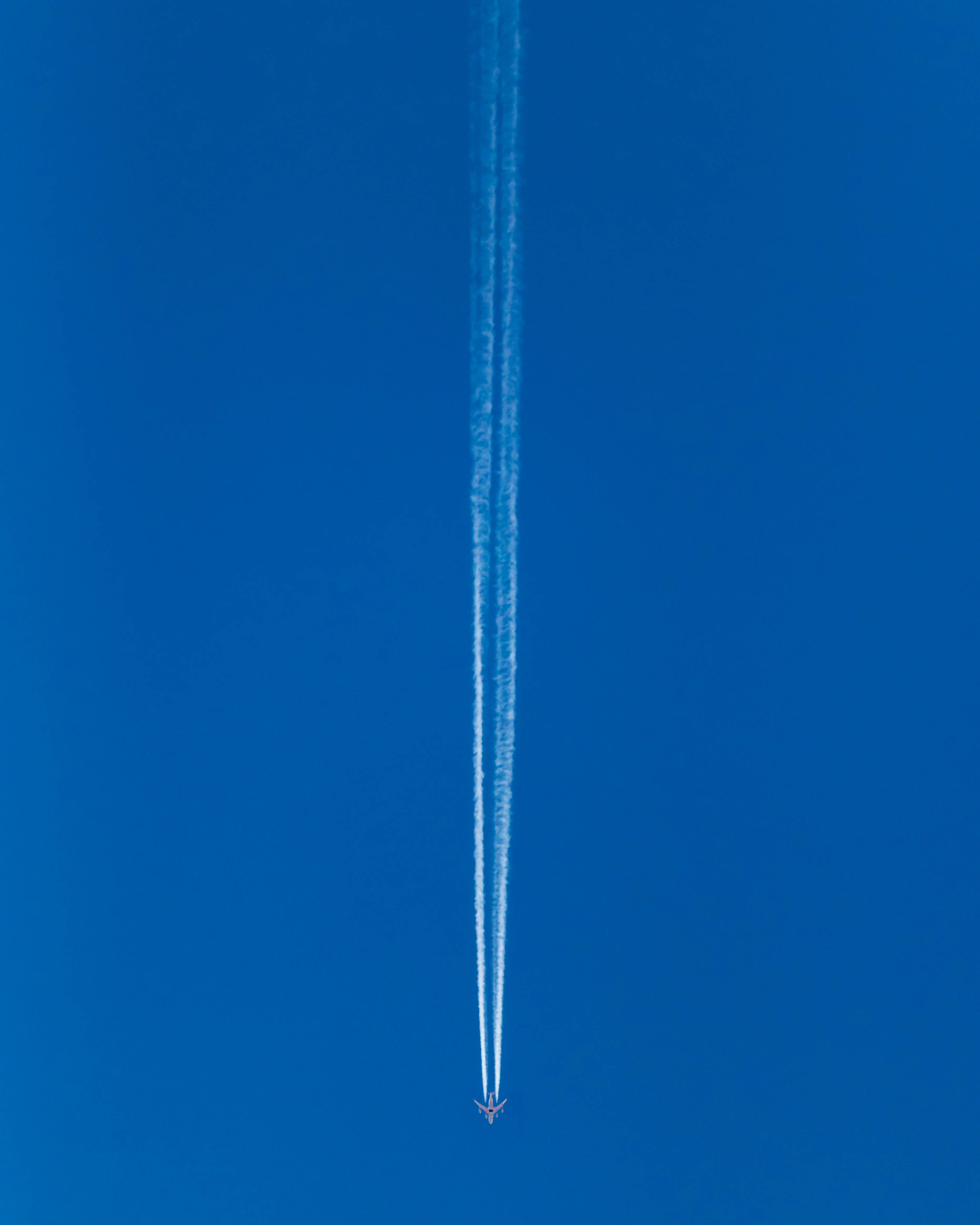 Fighter jet ascending with vapor trails against a clear blue sky.