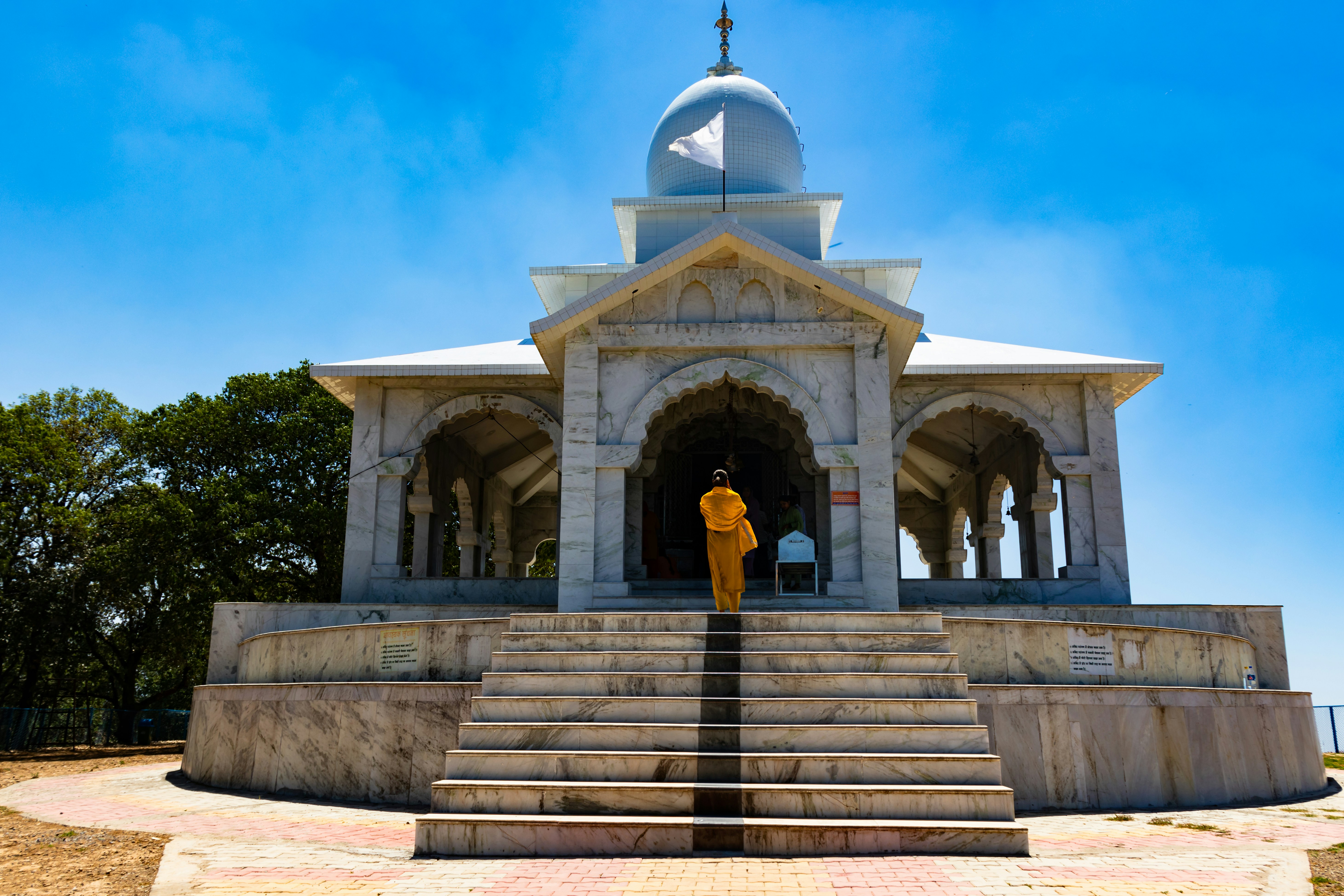 Person stands on steps leading to a marble pavilion under a clear blue sky.