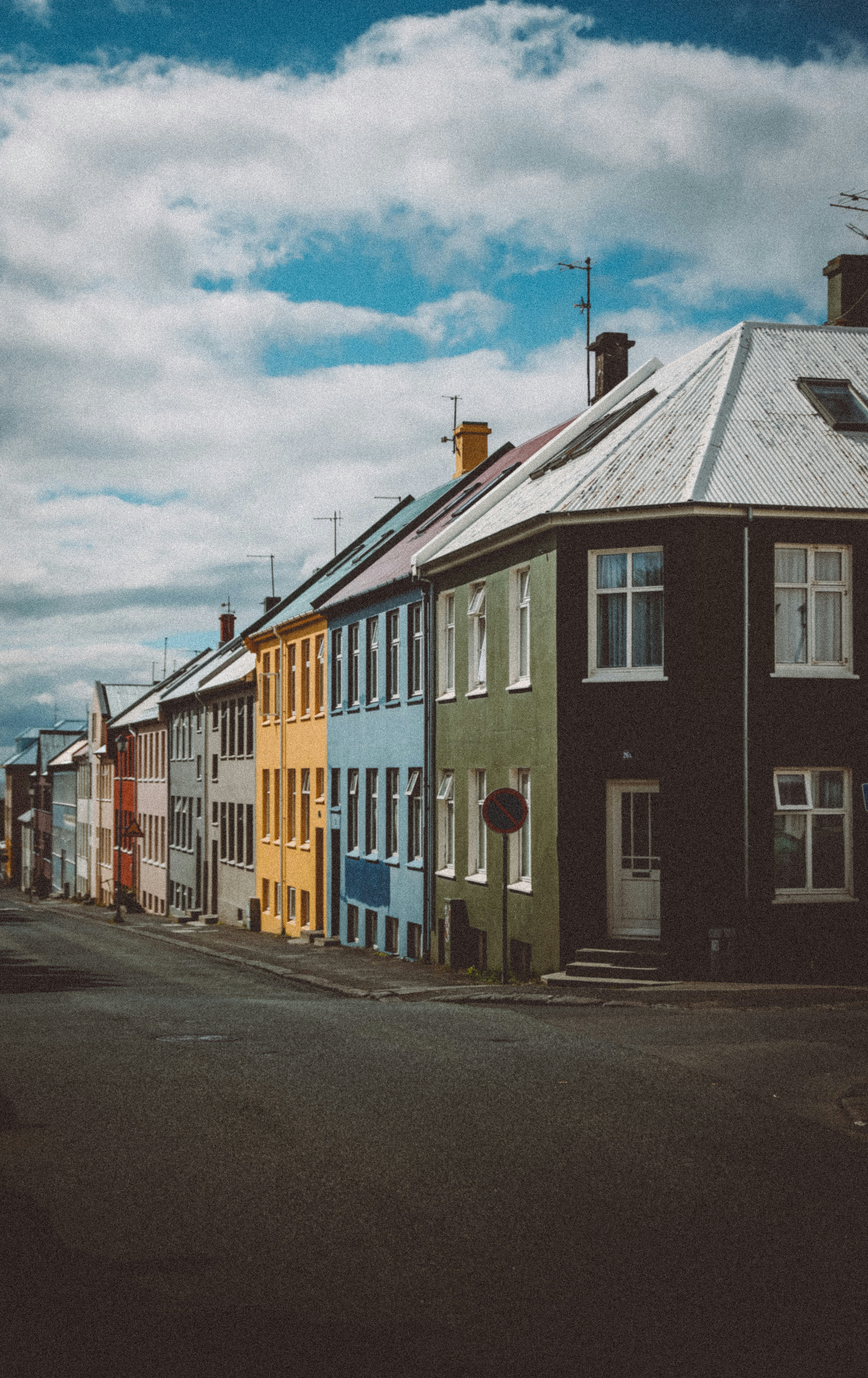 A line of colorful terraced houses along a quiet street under a partly cloudy sky.