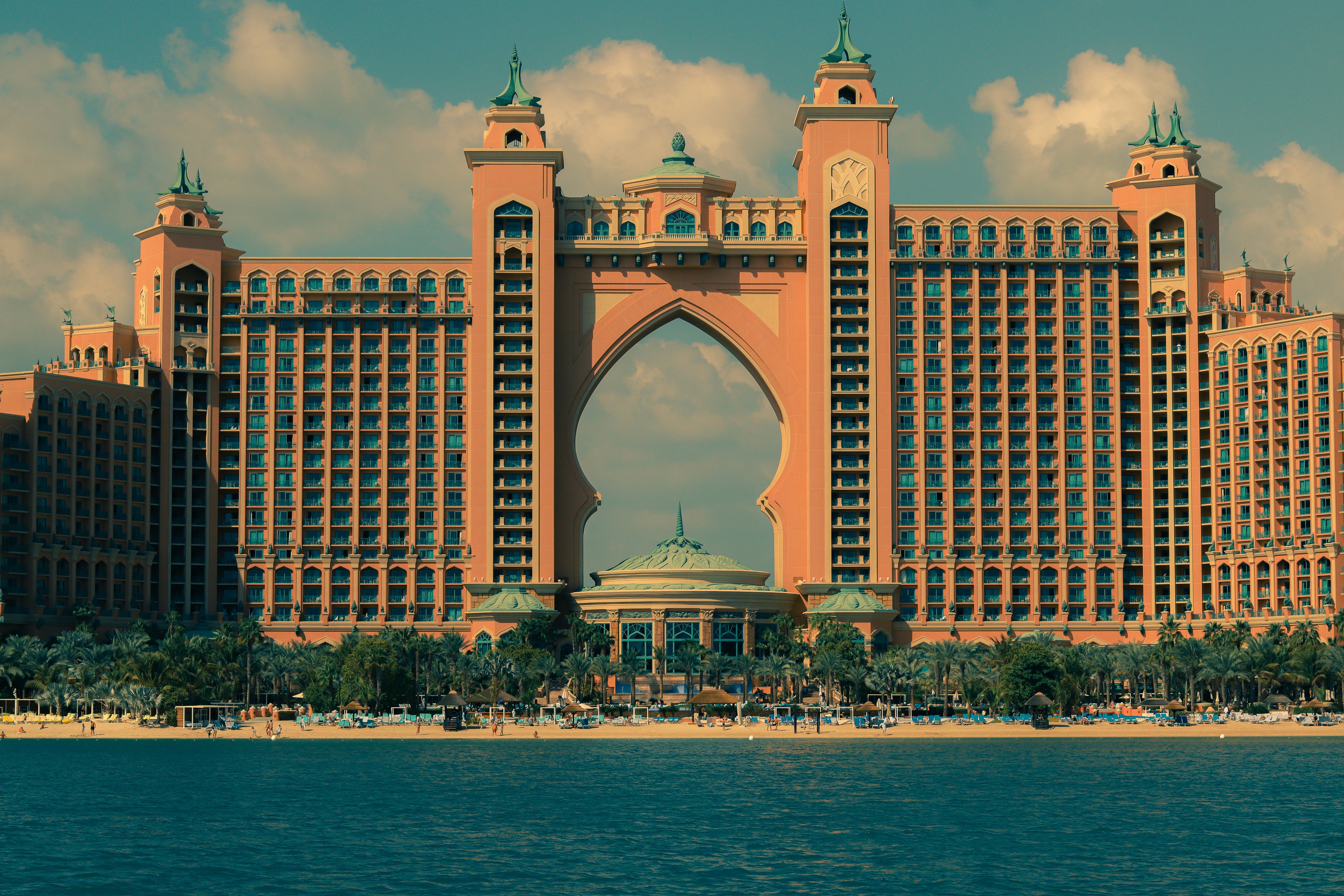 Grand hotel with central archway set against a vibrant blue sea under a partly cloudy sky.