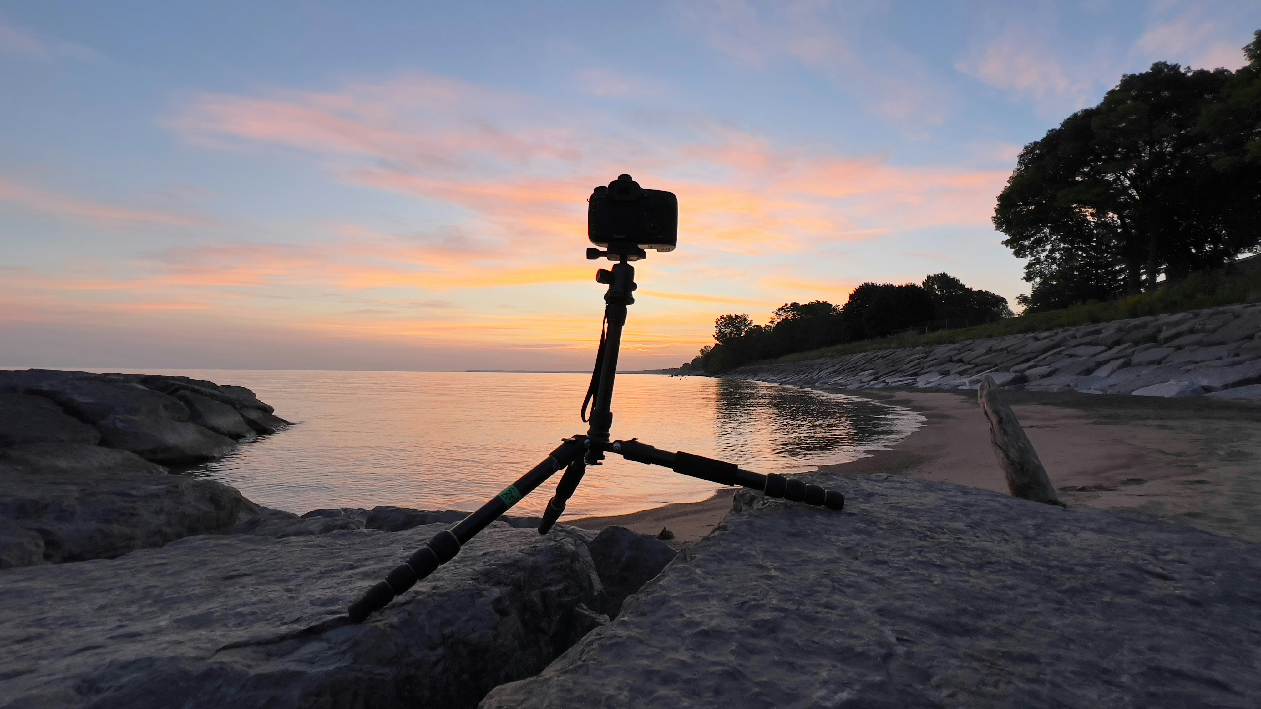 A tripod sitting on top of a rock next to a body of water photo – Free ...