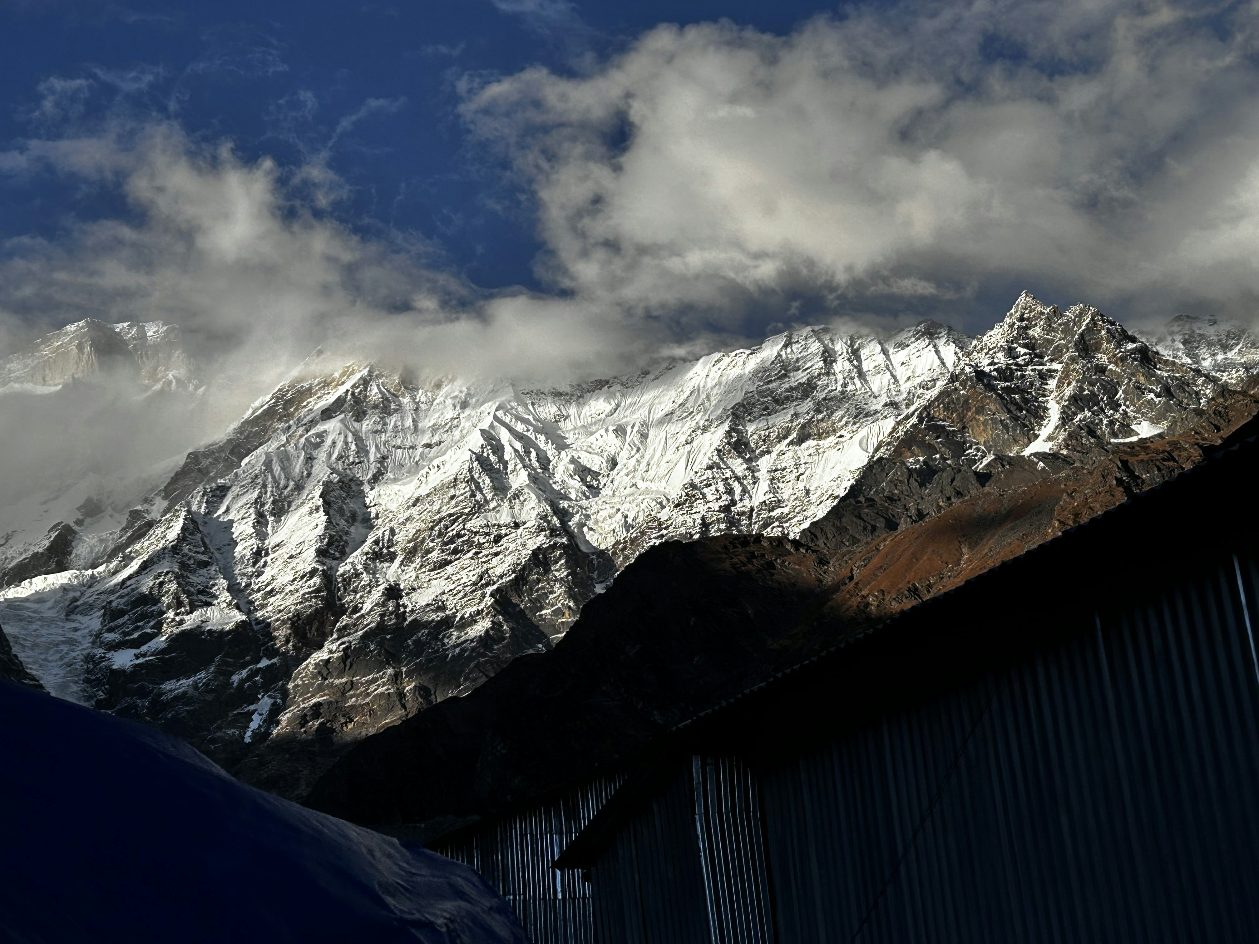 Snow-covered mountain range rises against a blue sky, framed by a dark corrugated-iron foreground.