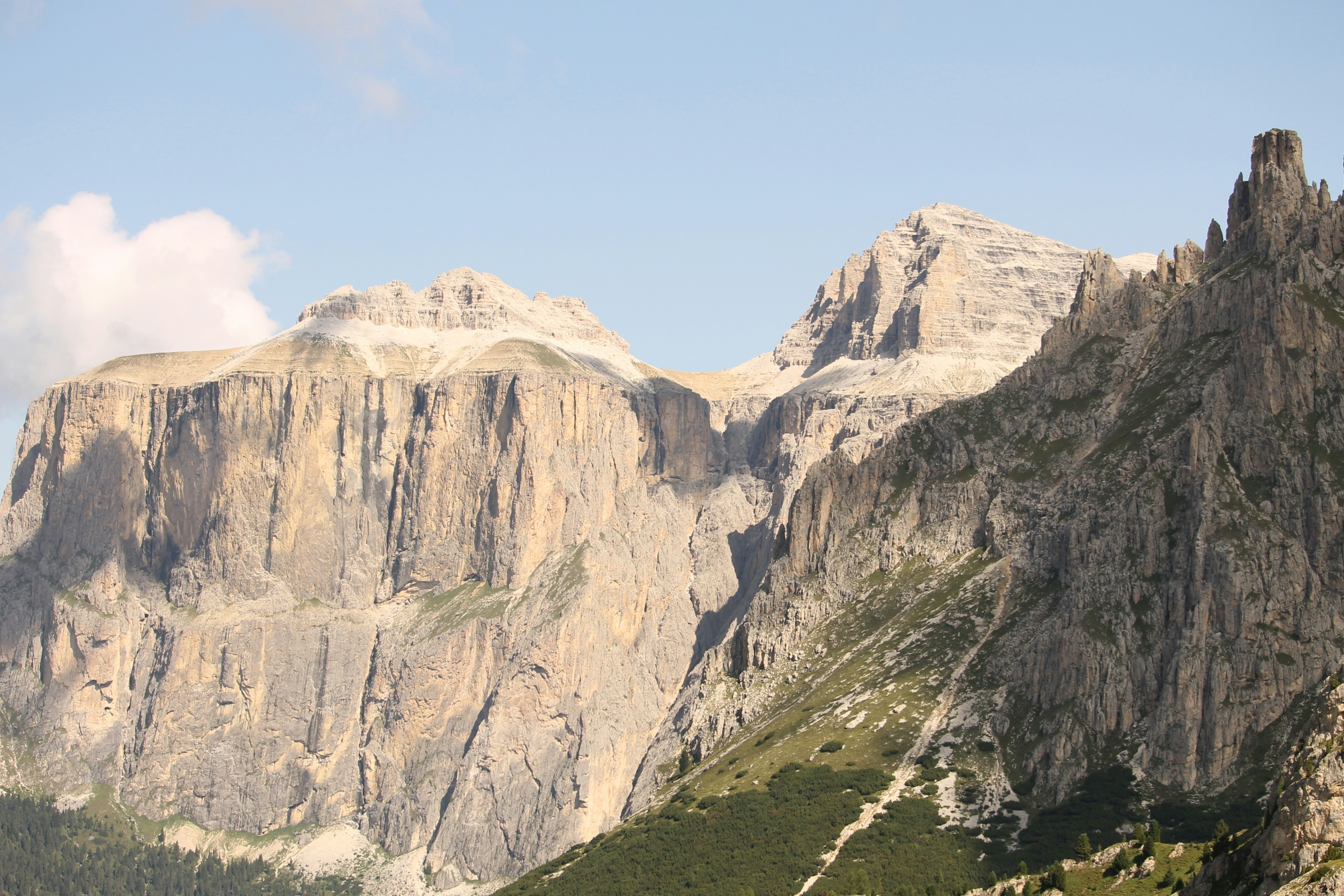 Sunlit Dolomite mountains with rugged cliffs and sharp peaks against a clear blue sky.