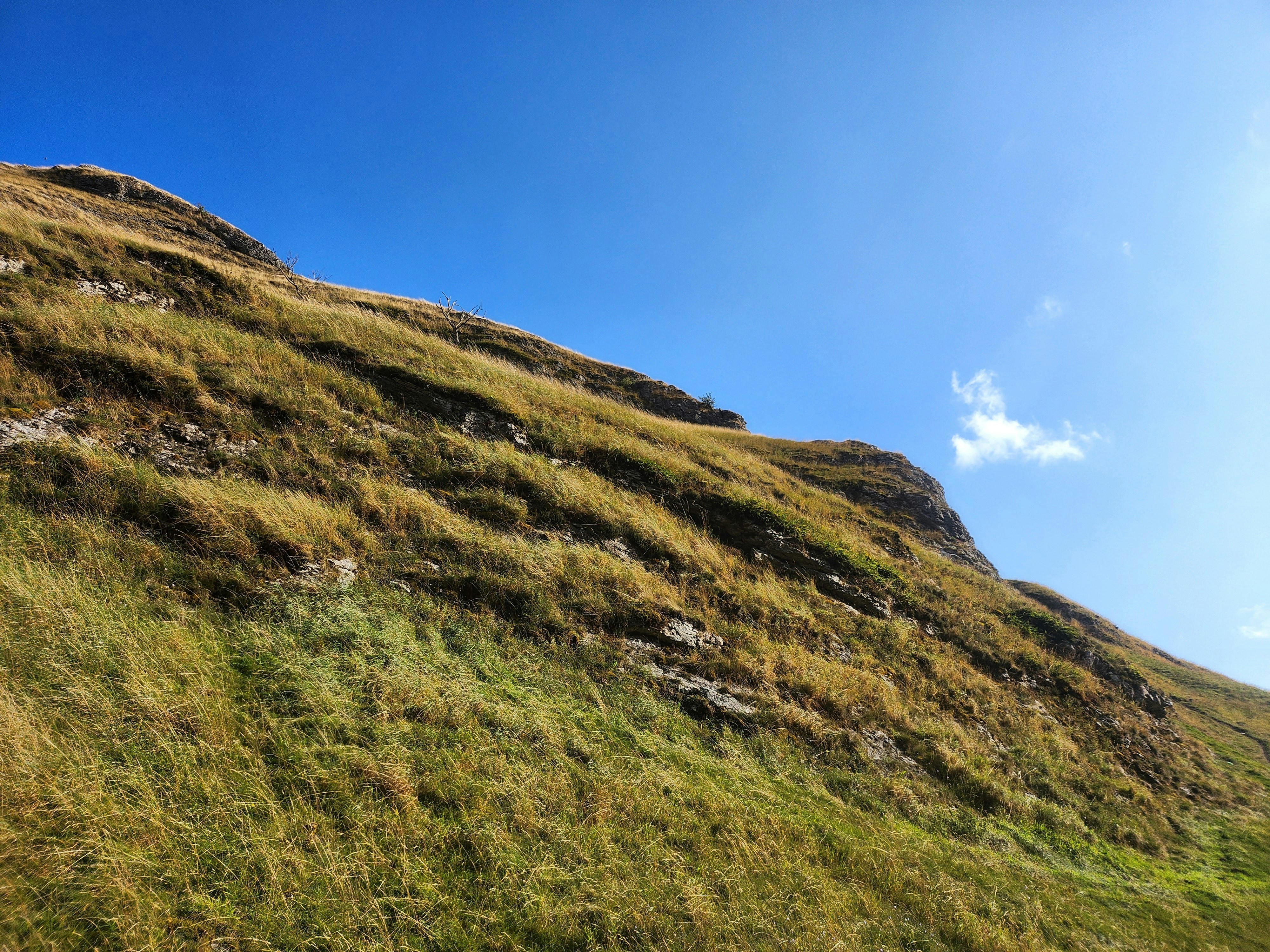 Grassy hillside with layered rock formations against a vibrant blue sky.