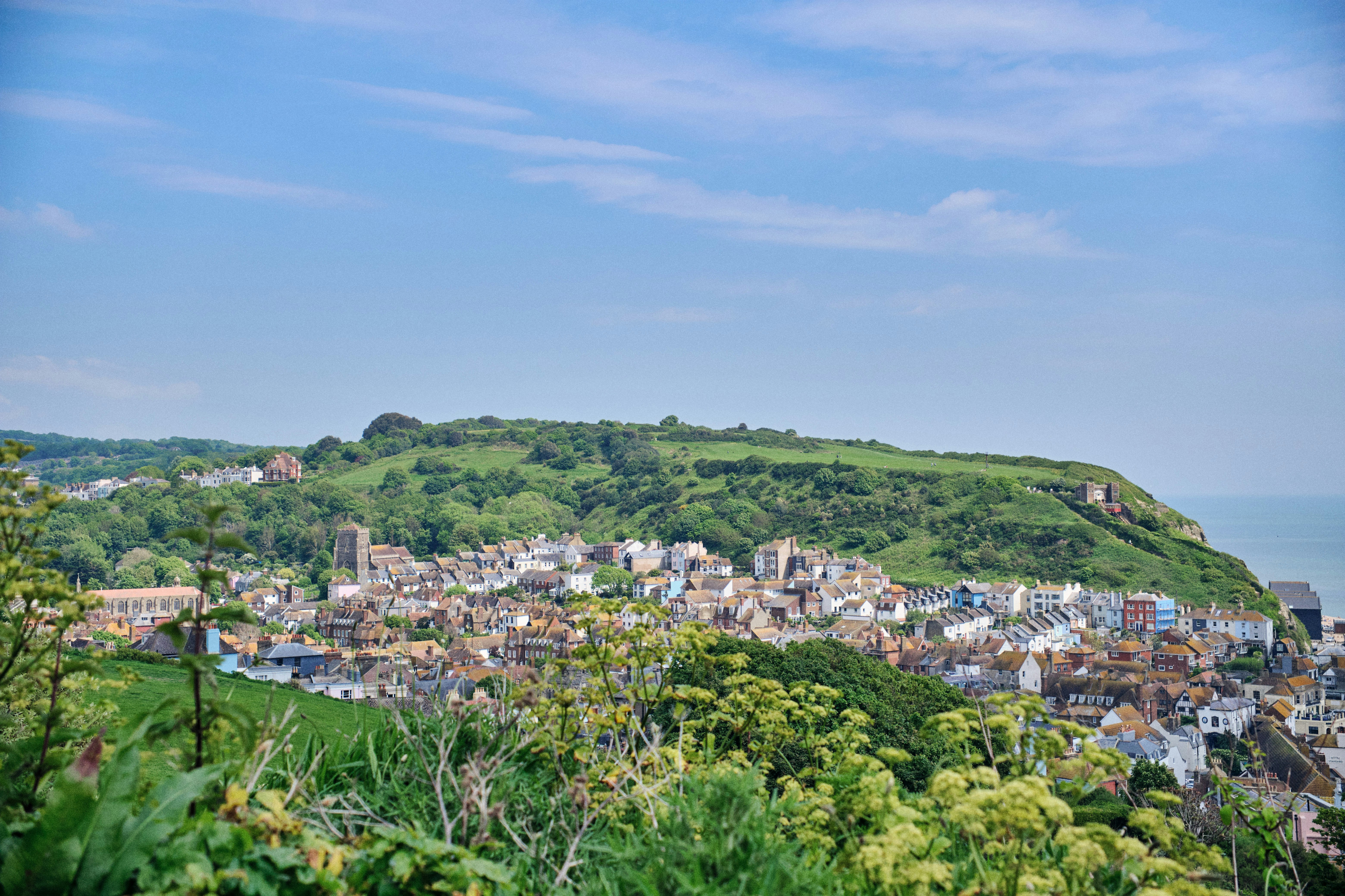 Coastal town nestled against green hills under a clear blue sky.
