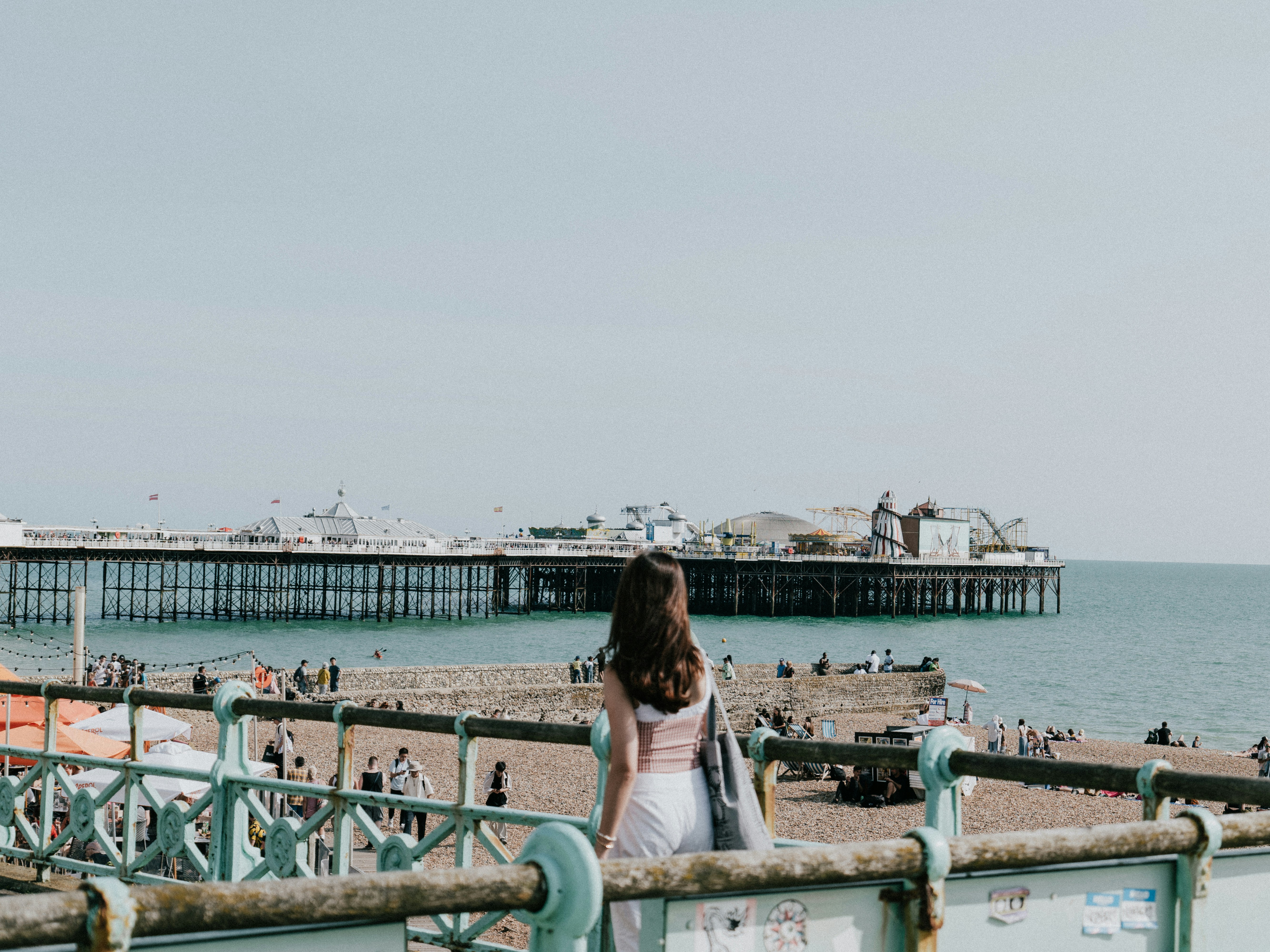 Pierside Reverie: A Woman in White Overlooking the Busy Seaside Pier
