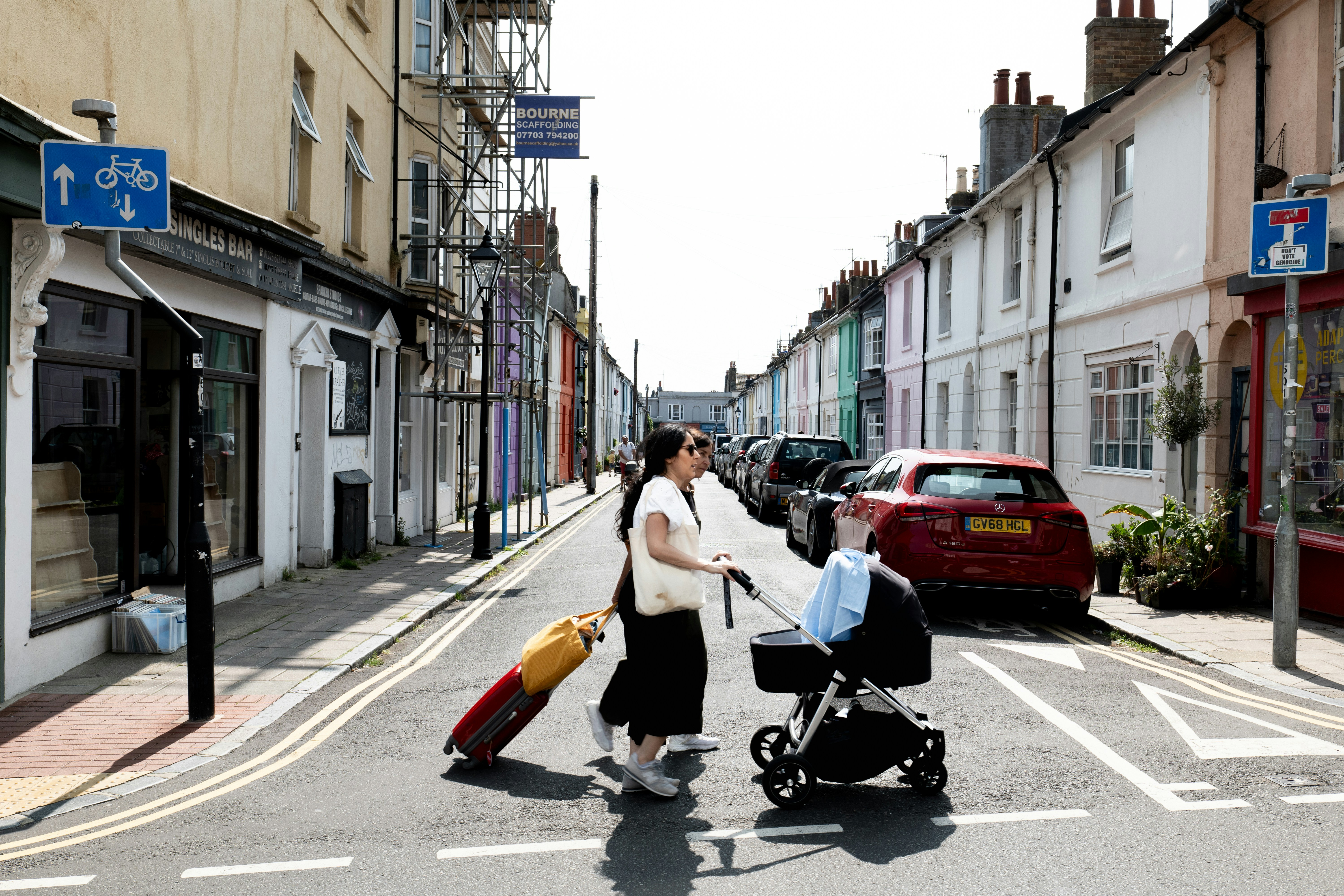 Sunlit Crossings: A Woman with Stroller and Luggage at a Quiet Town Street